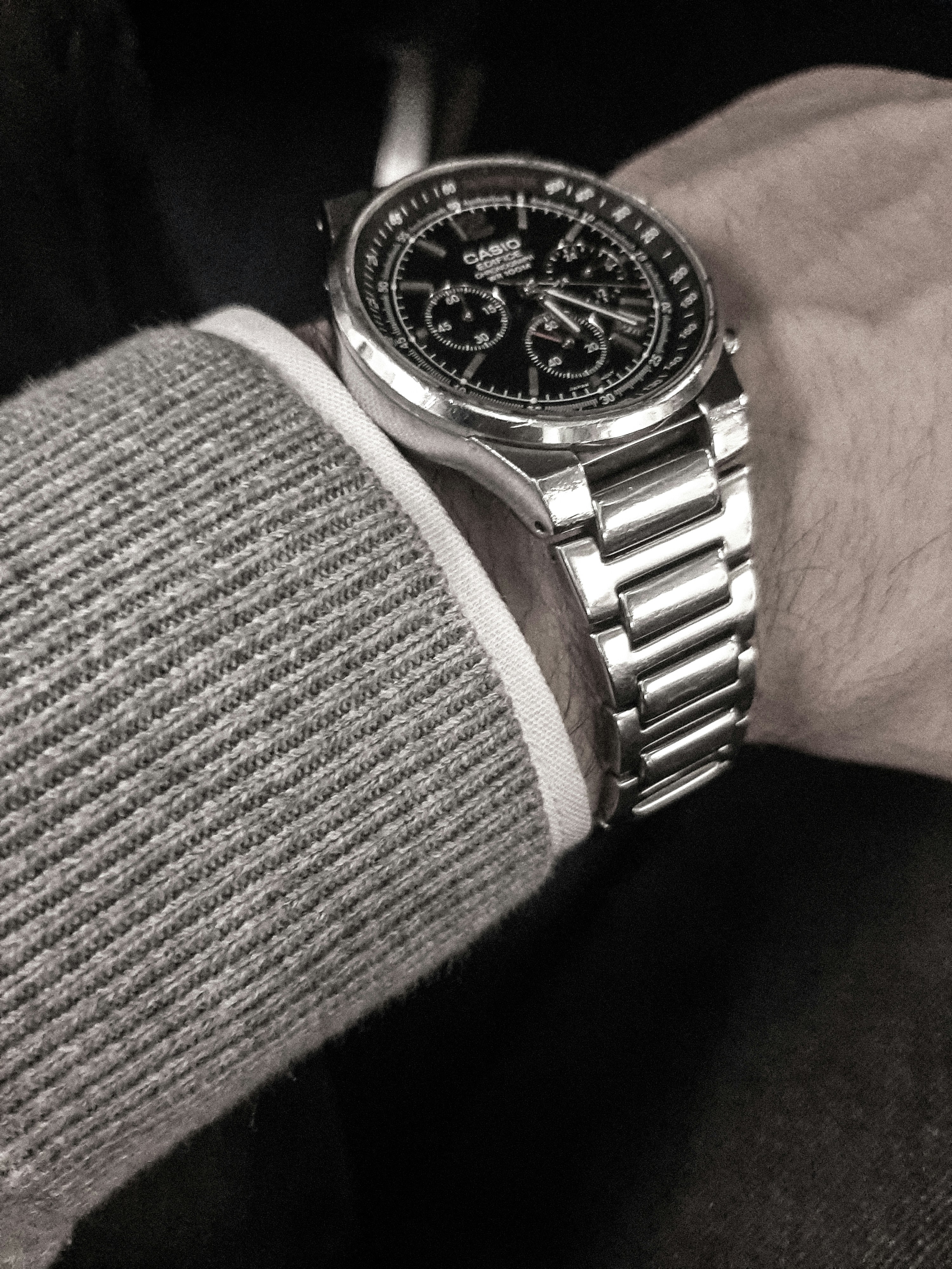Close-up of a stainless steel Casio chronograph watch worn over a ribbed knit sleeve, captured in black and white.
