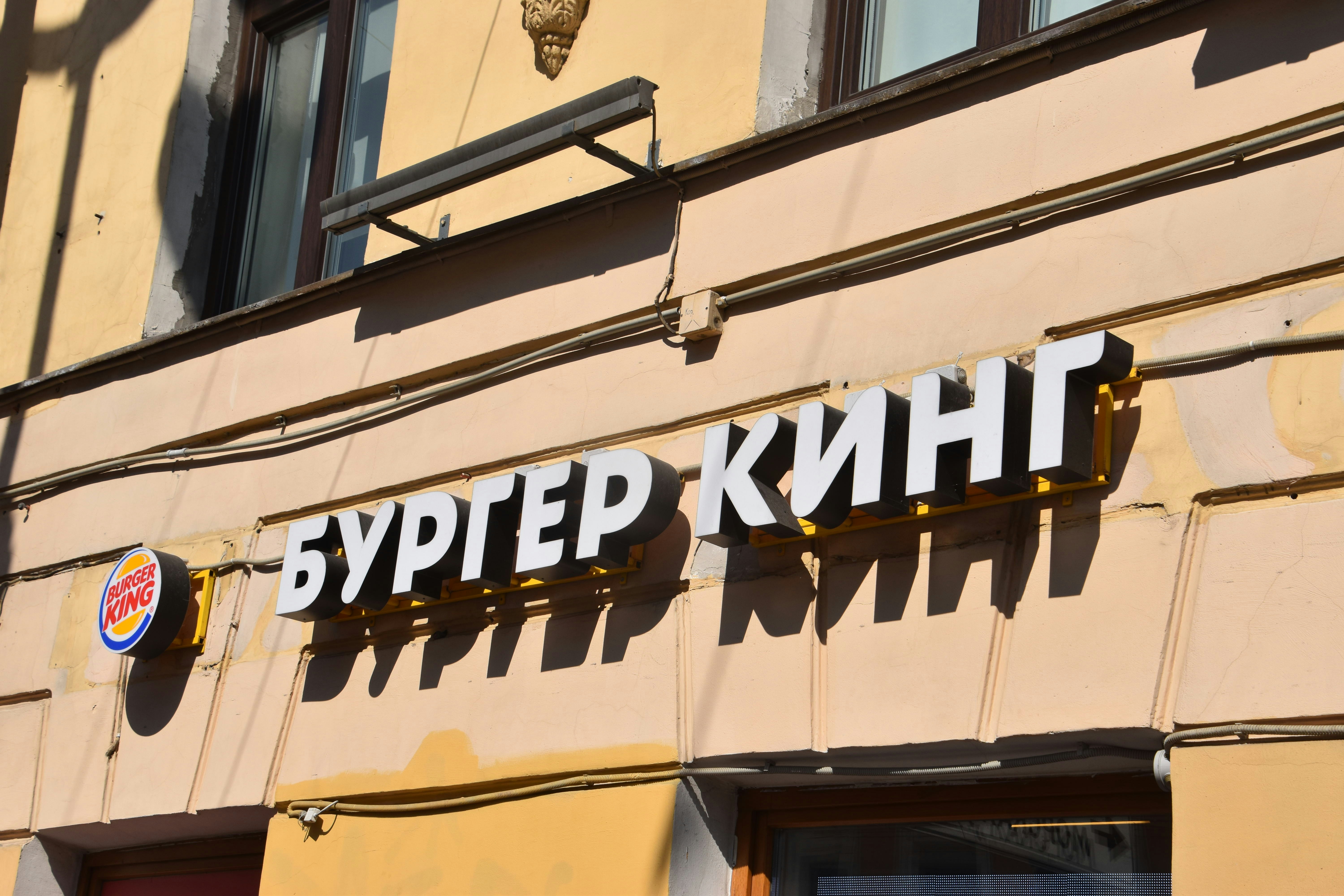 Bold signage of a fast-food restaurant against a sunlit wall, showcasing both Cyrillic and English text. The contrasting colors enhance visibility.