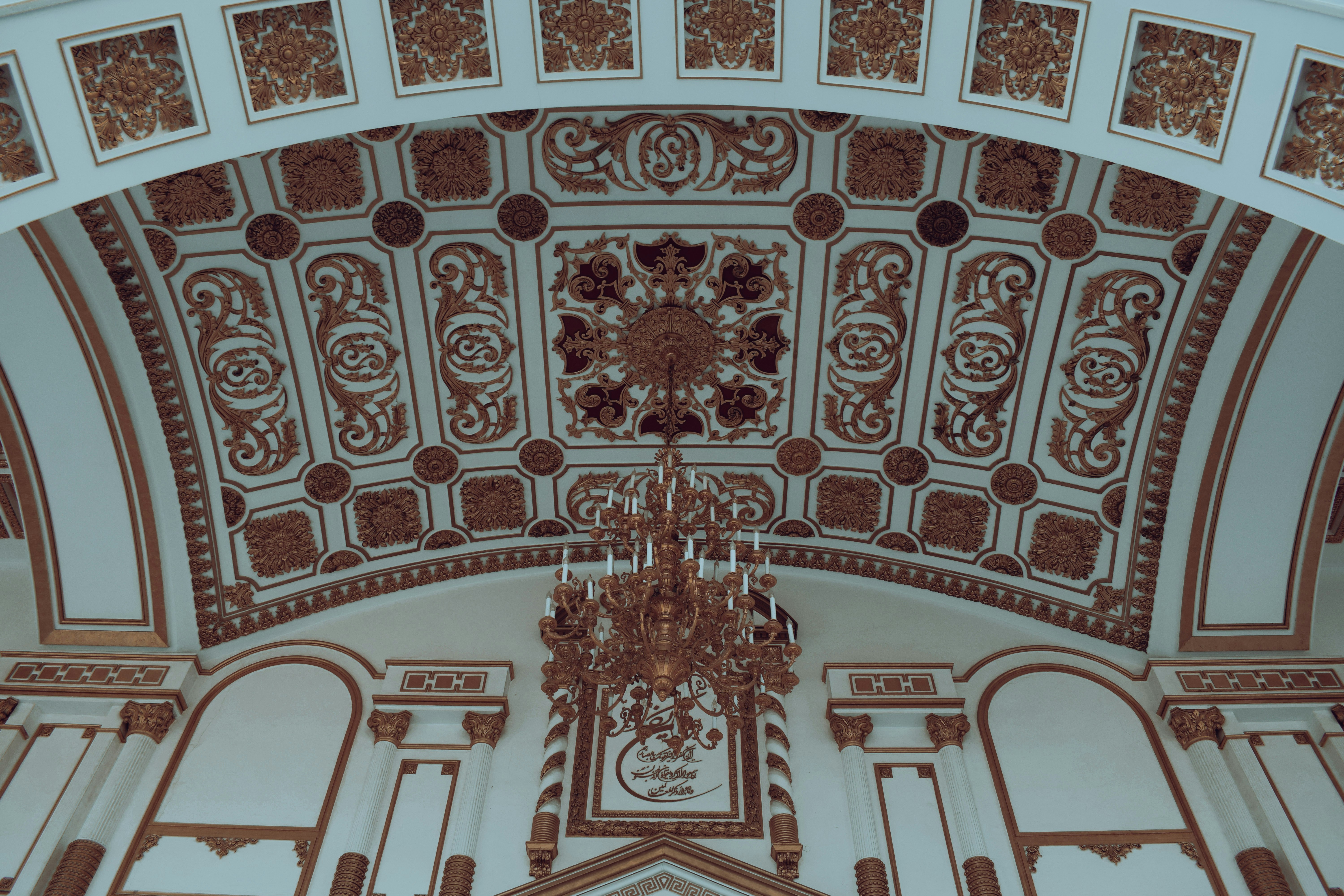 Intricately designed ceiling with symmetrical patterns and a central chandelier in warm tones.