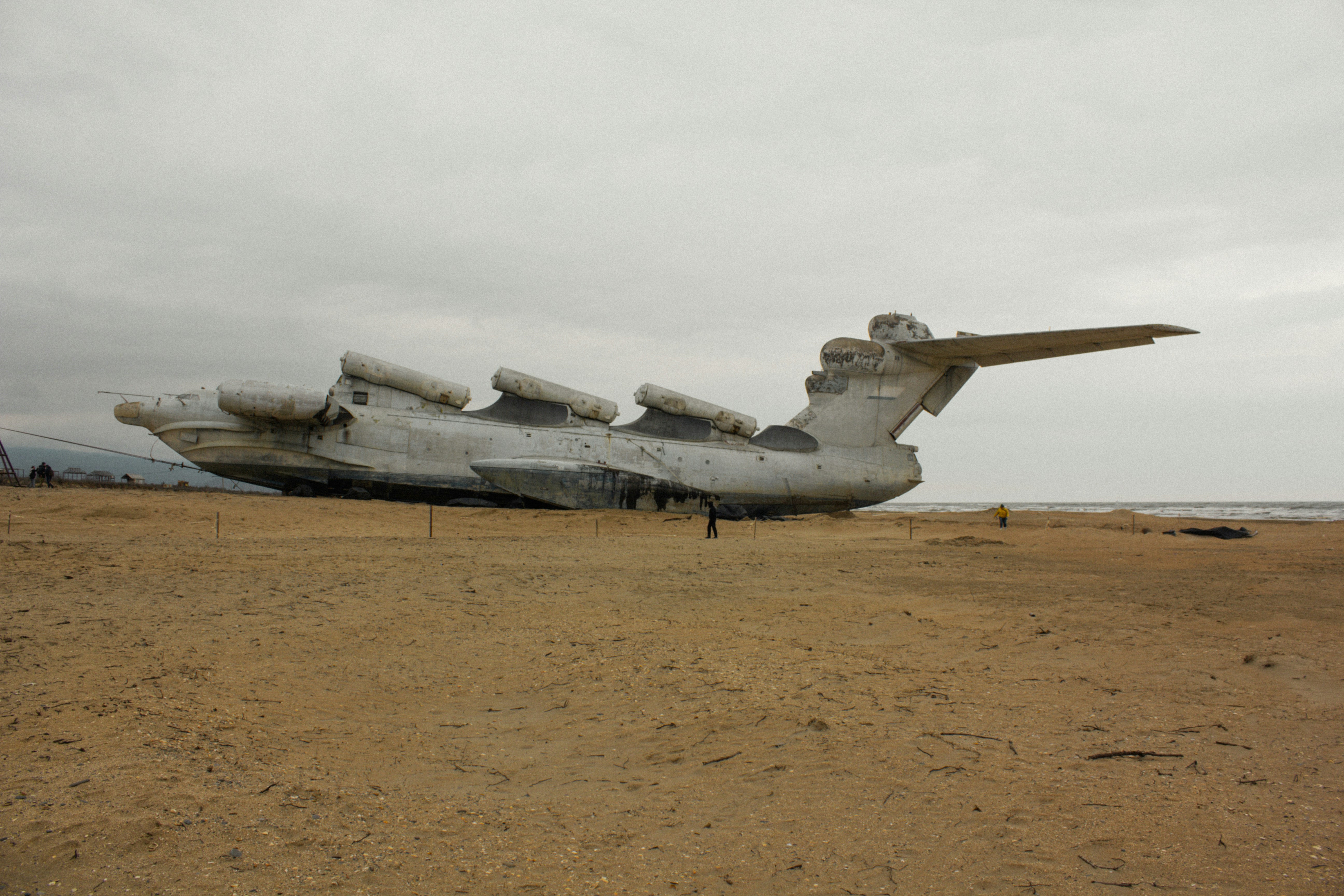 Abandoned Ekranoplan rests on a barren landscape under a cloudy sky.