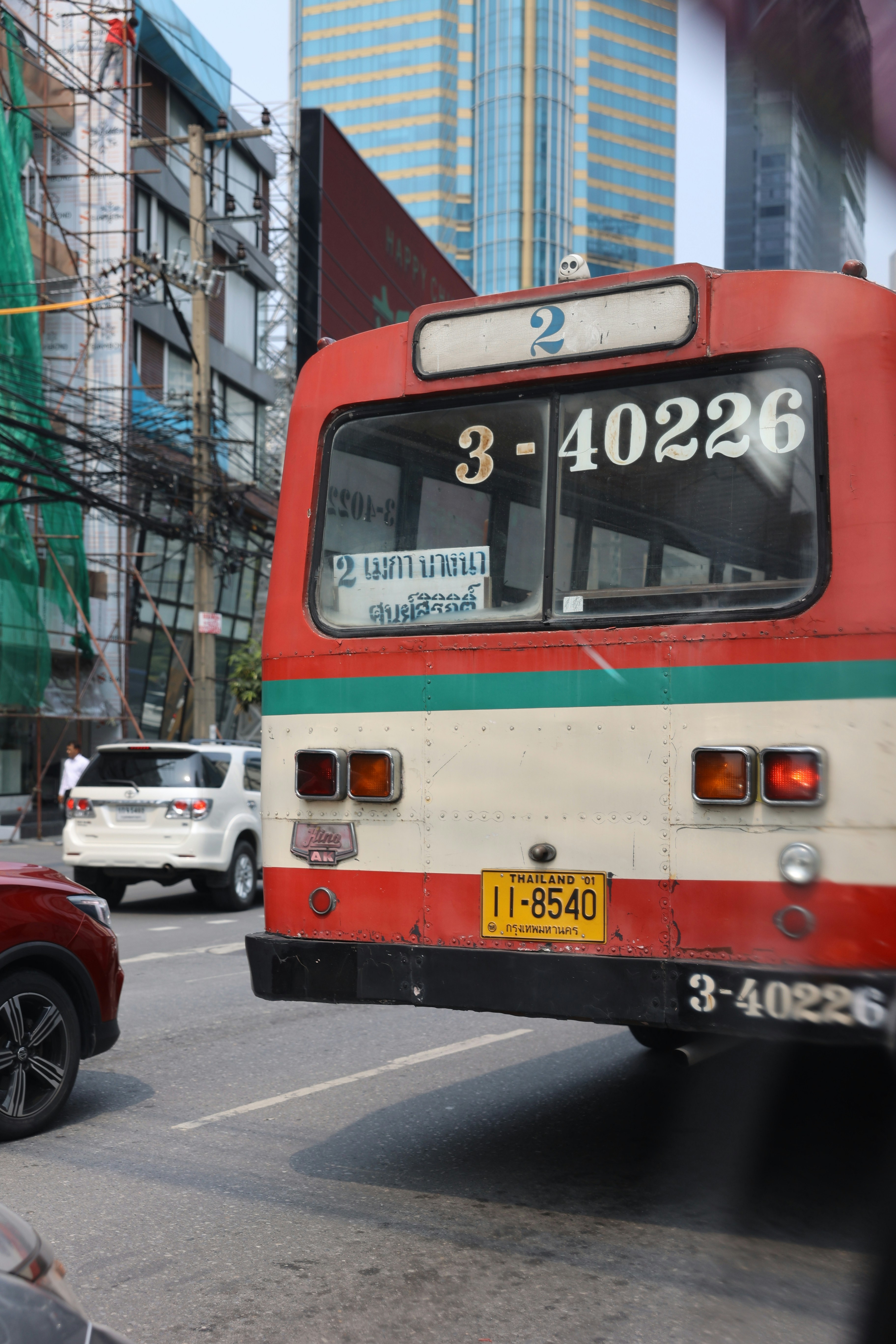 A city bus with a bright red and white design navigates through a bustling urban landscape, showcasing the daily rhythm of city life.