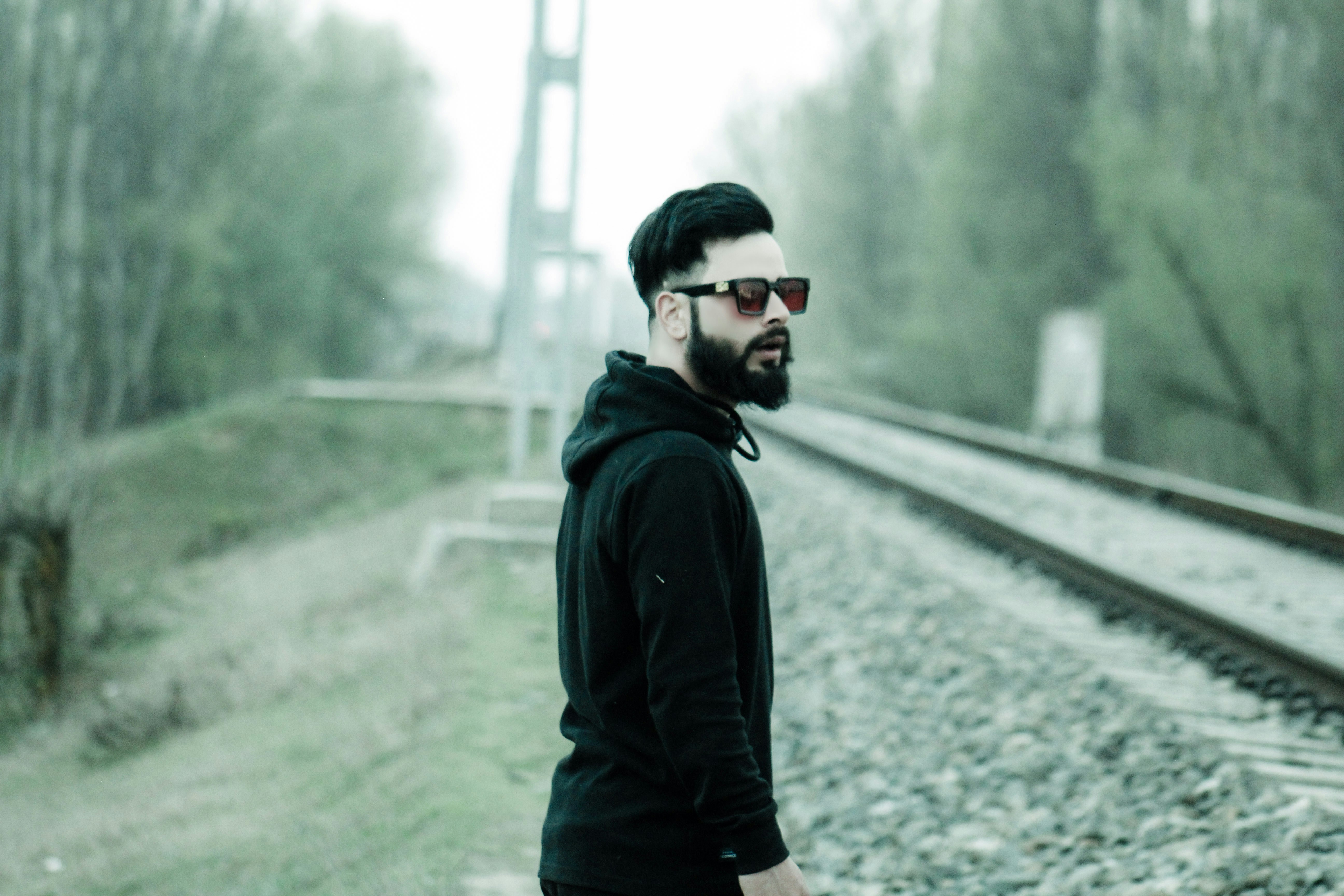 A man with a beard and sunglasses standing on a train track photo ...