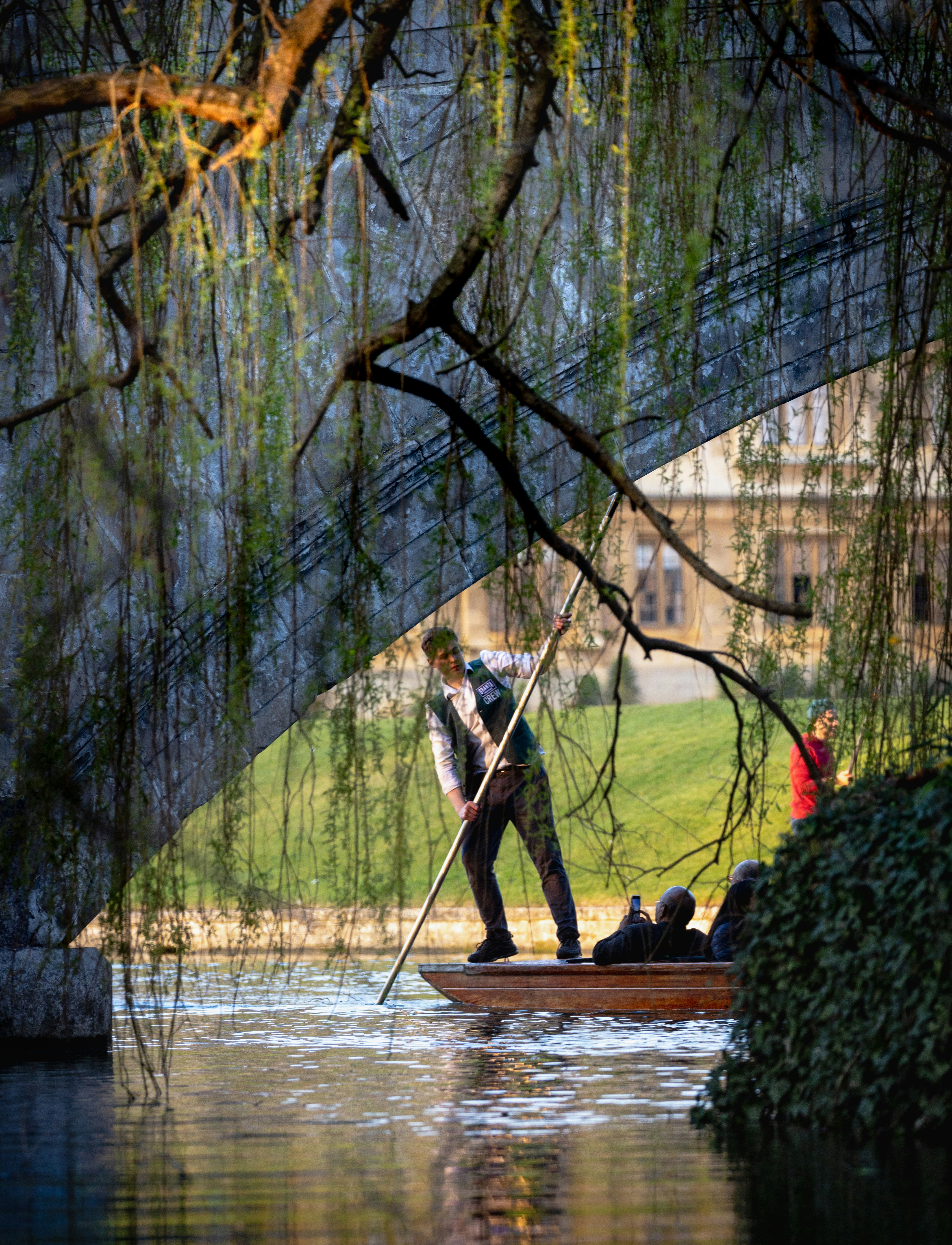 A gondolier skillfully navigates a serene waterway beneath a gracefully arched bridge, surrounded by lush greenery and soft reflections. 