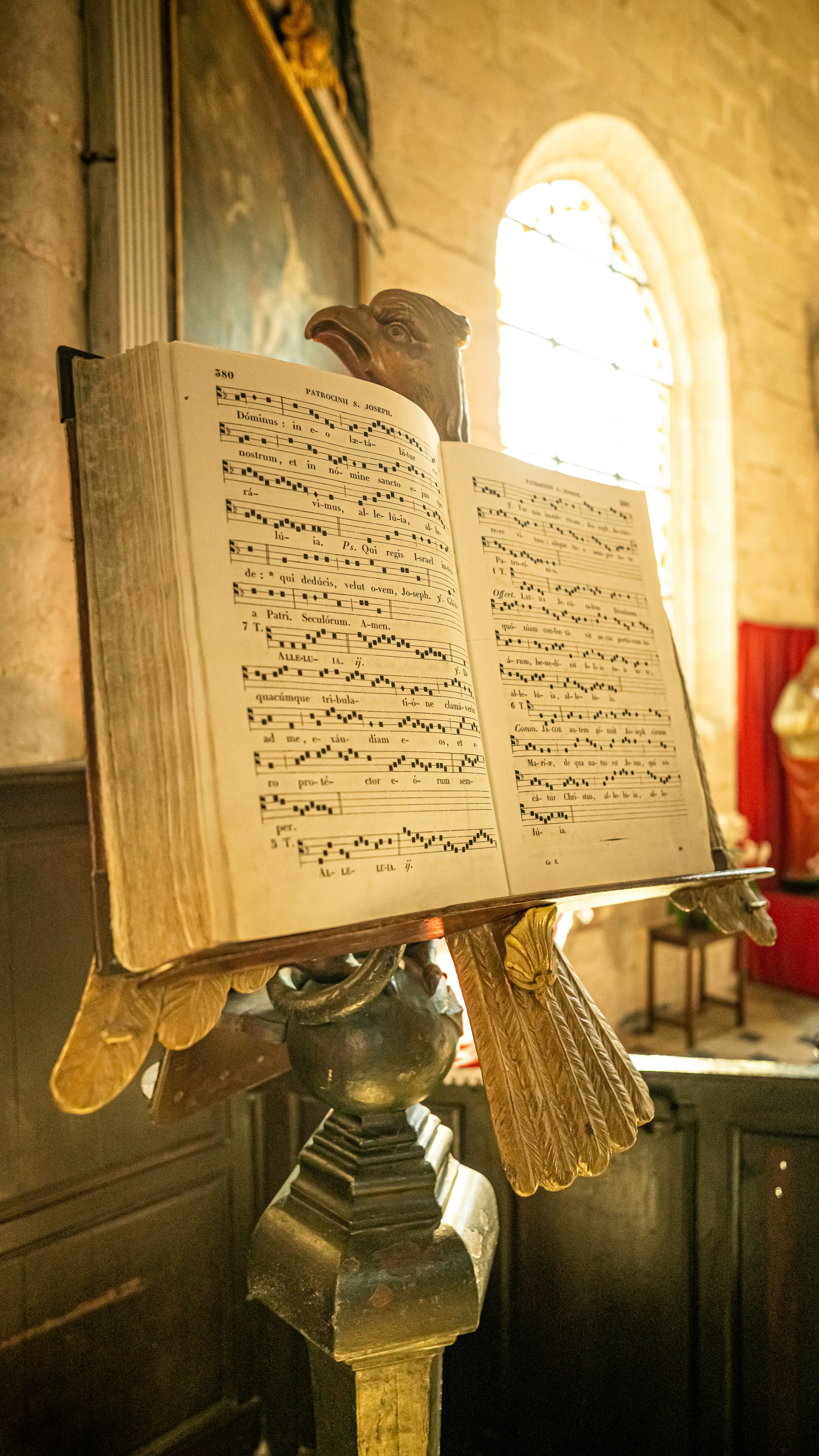 An intricately designed music stand featuring an open book of sheet music, illuminated by soft natural light, set against a backdrop of historical architecture.