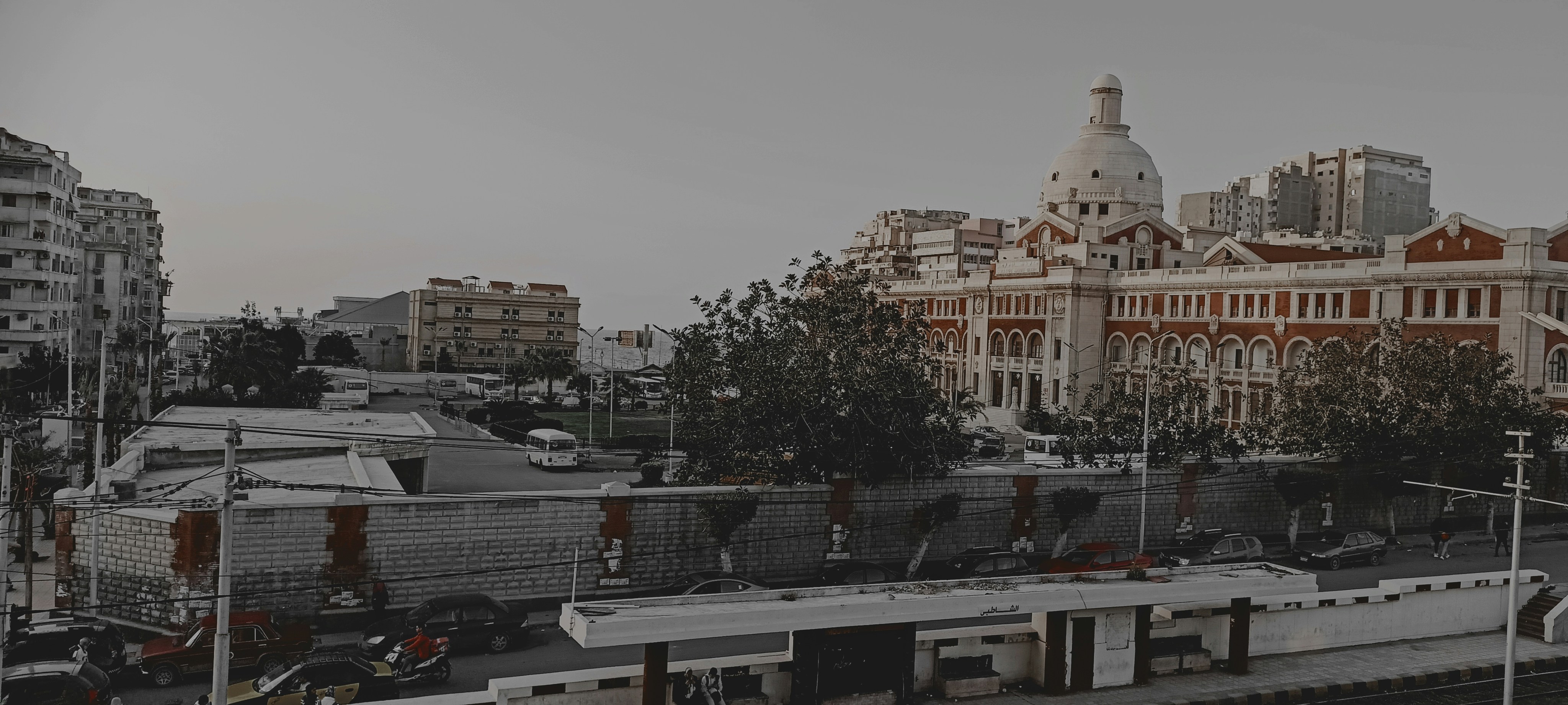 Train moving alongside towering urban structures under a gray sky.