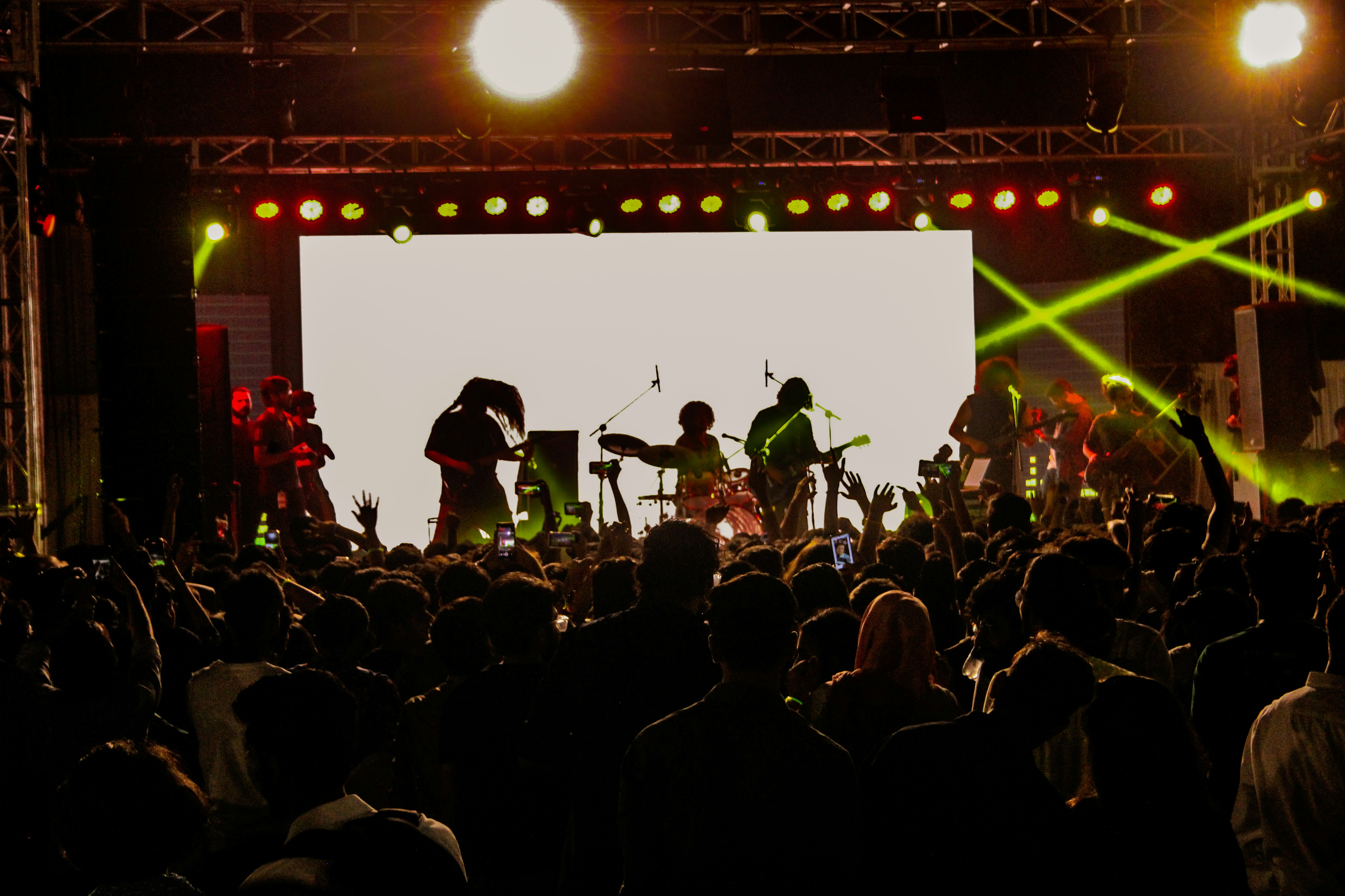 Silhouetted band performing on a stage with bright backlighting and vibrant crowd.