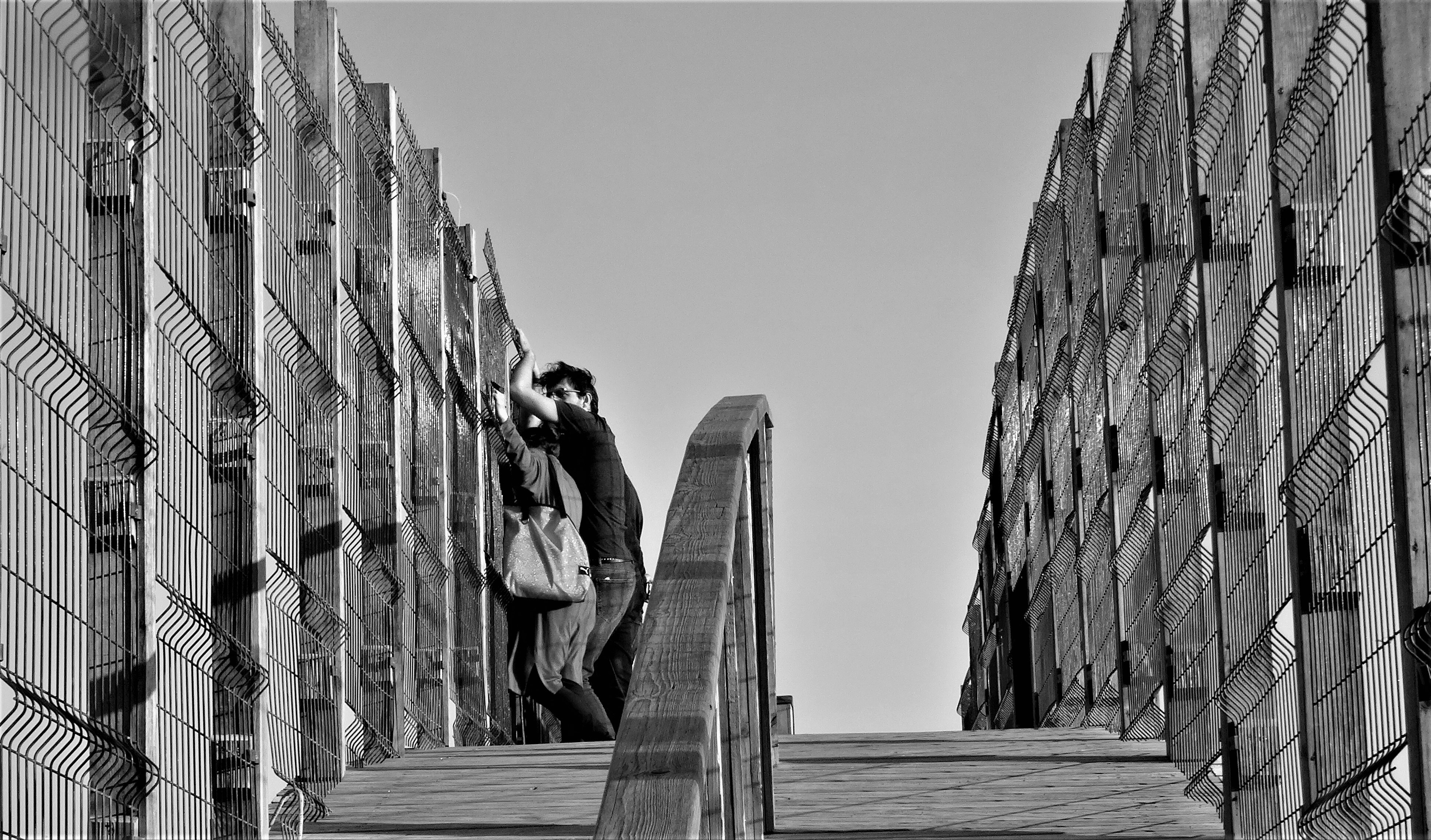Couple sharing a tender moment on a wooden bridge surrounded by towering, textured walls of urban architecture.