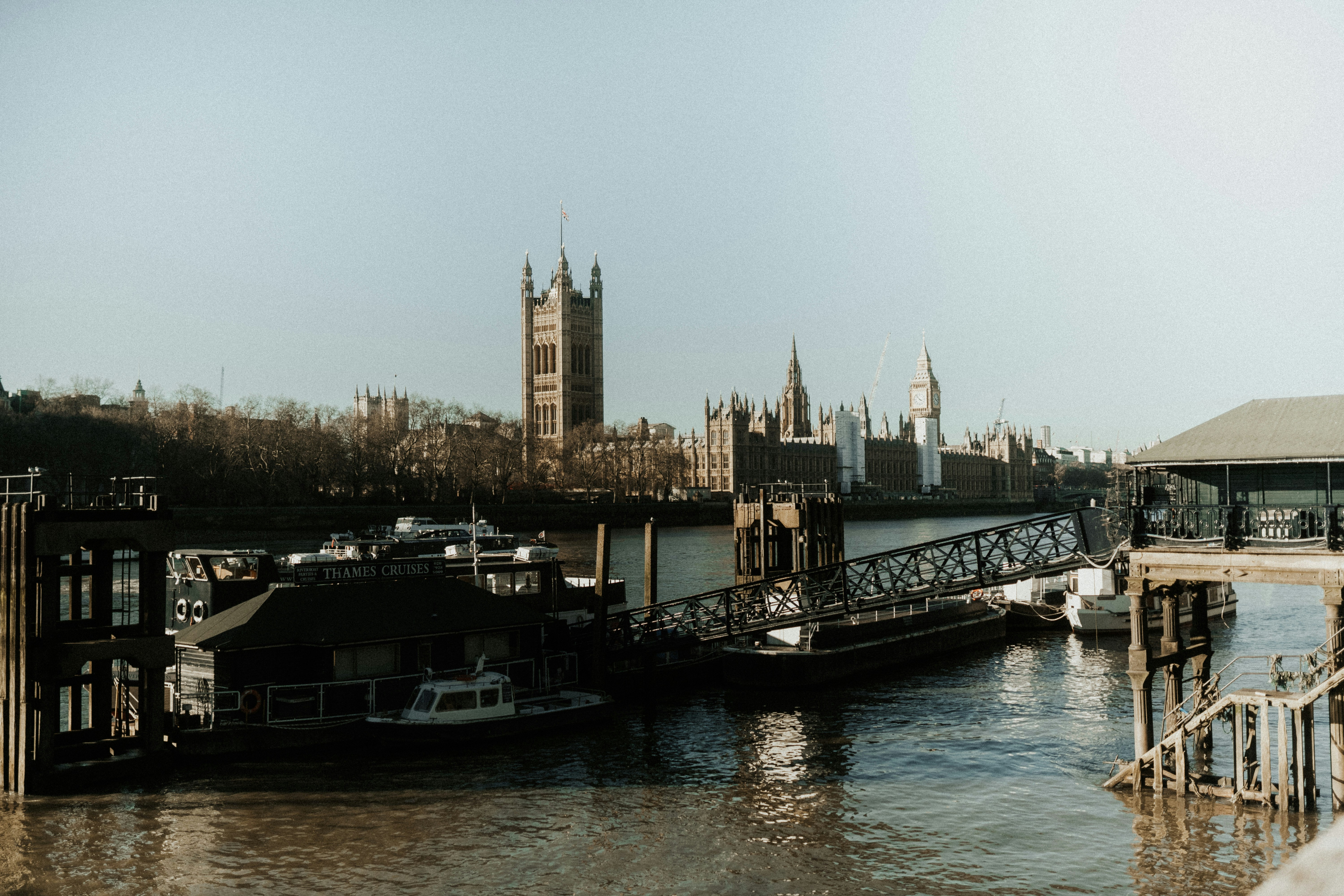 Historic buildings lining the Thames River with boats docked at a pier, showcasing a blend of architecture and waterway activity.