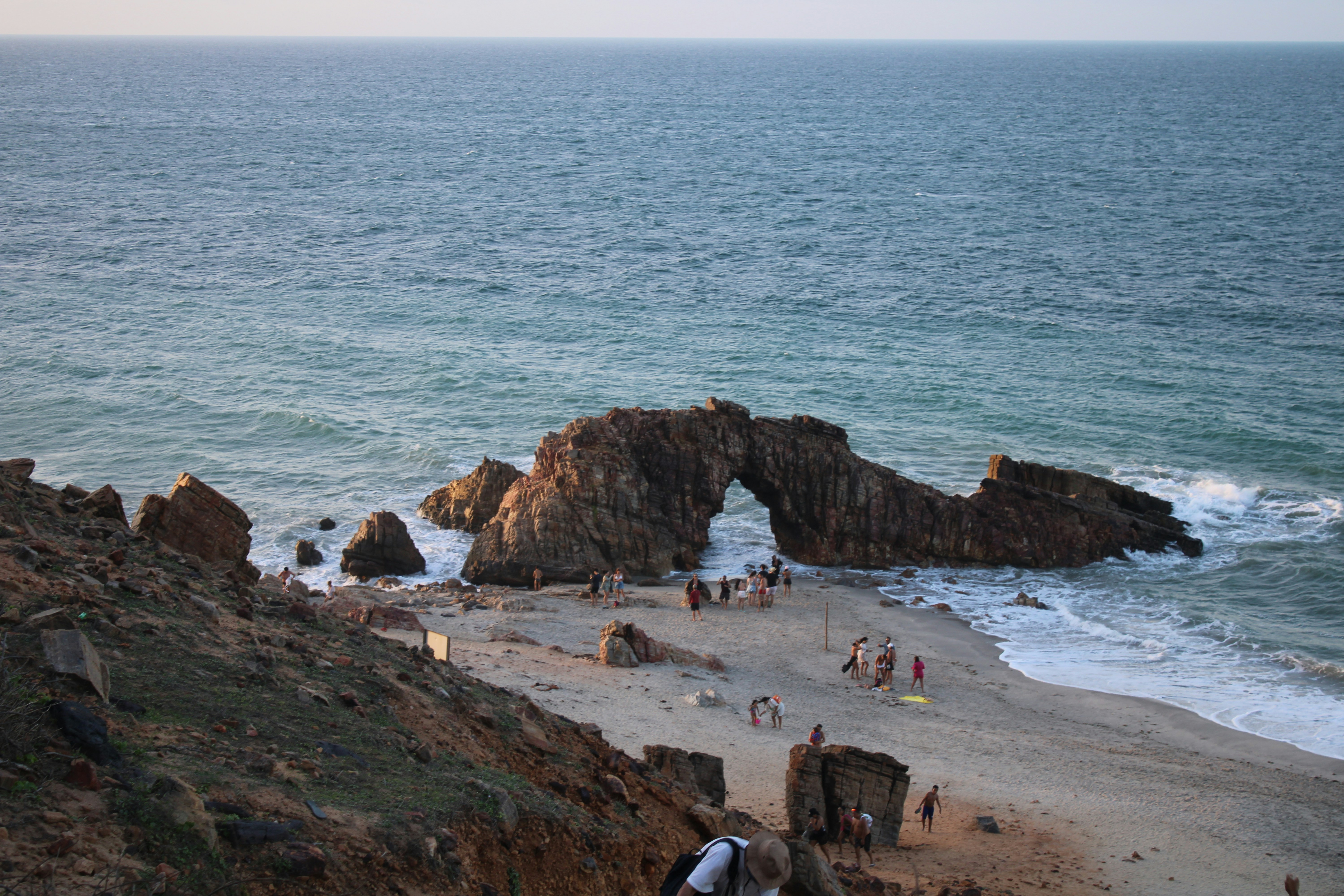 Sea Arch Rendezvous: Sunlit Beachgoers at a Weathered Coastal Gate