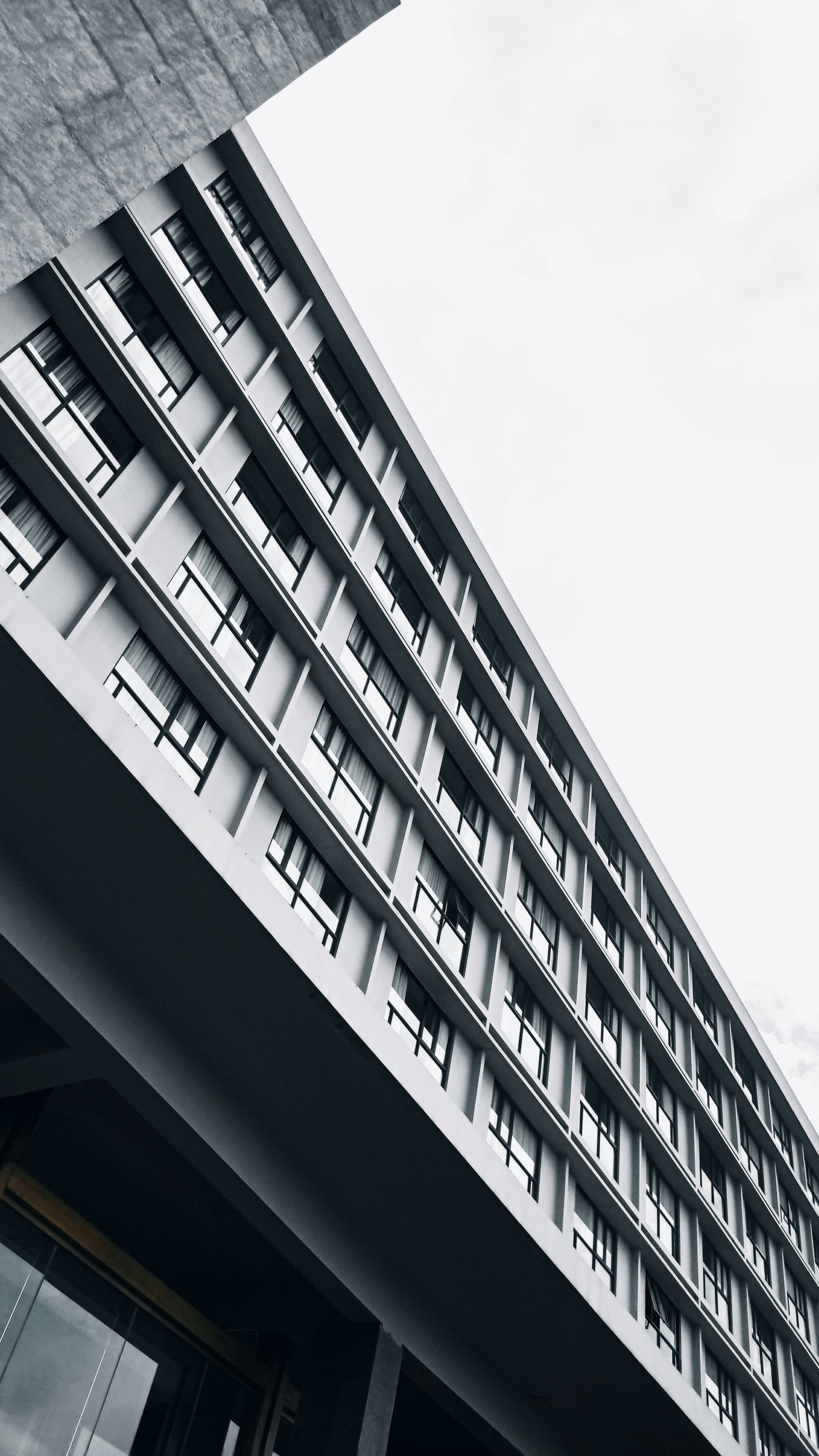 Abstract view of a contemporary building showcasing its angular design and repetitive window patterns against a cloudy sky.