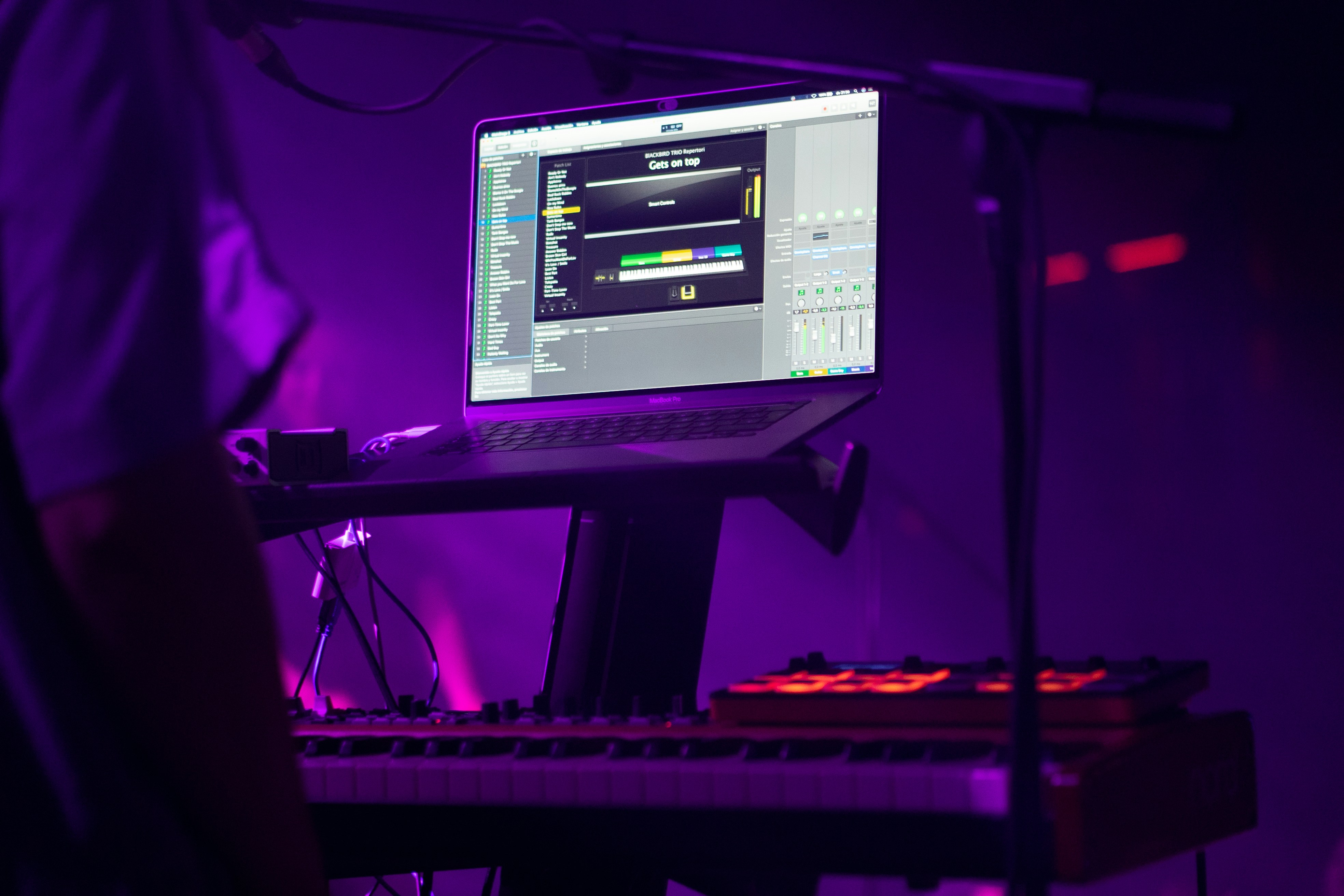 Keyboard and laptop setup illuminated by purple stage lights, showcasing a digital audio interface in use.