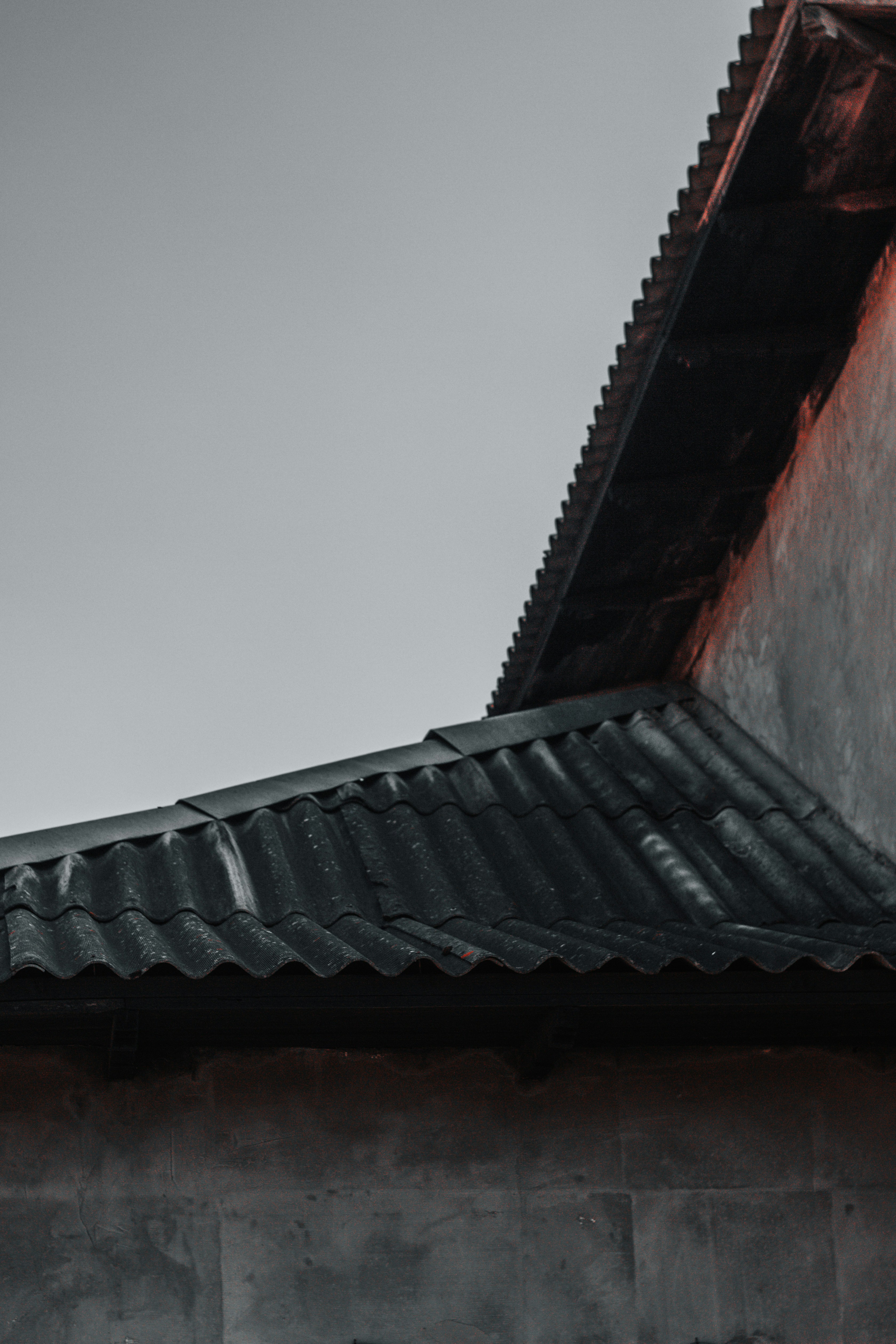 Close-up of a textured roofline against a muted sky, highlighting the interplay of light and shadow. The image captures the architectural details of a building's design.