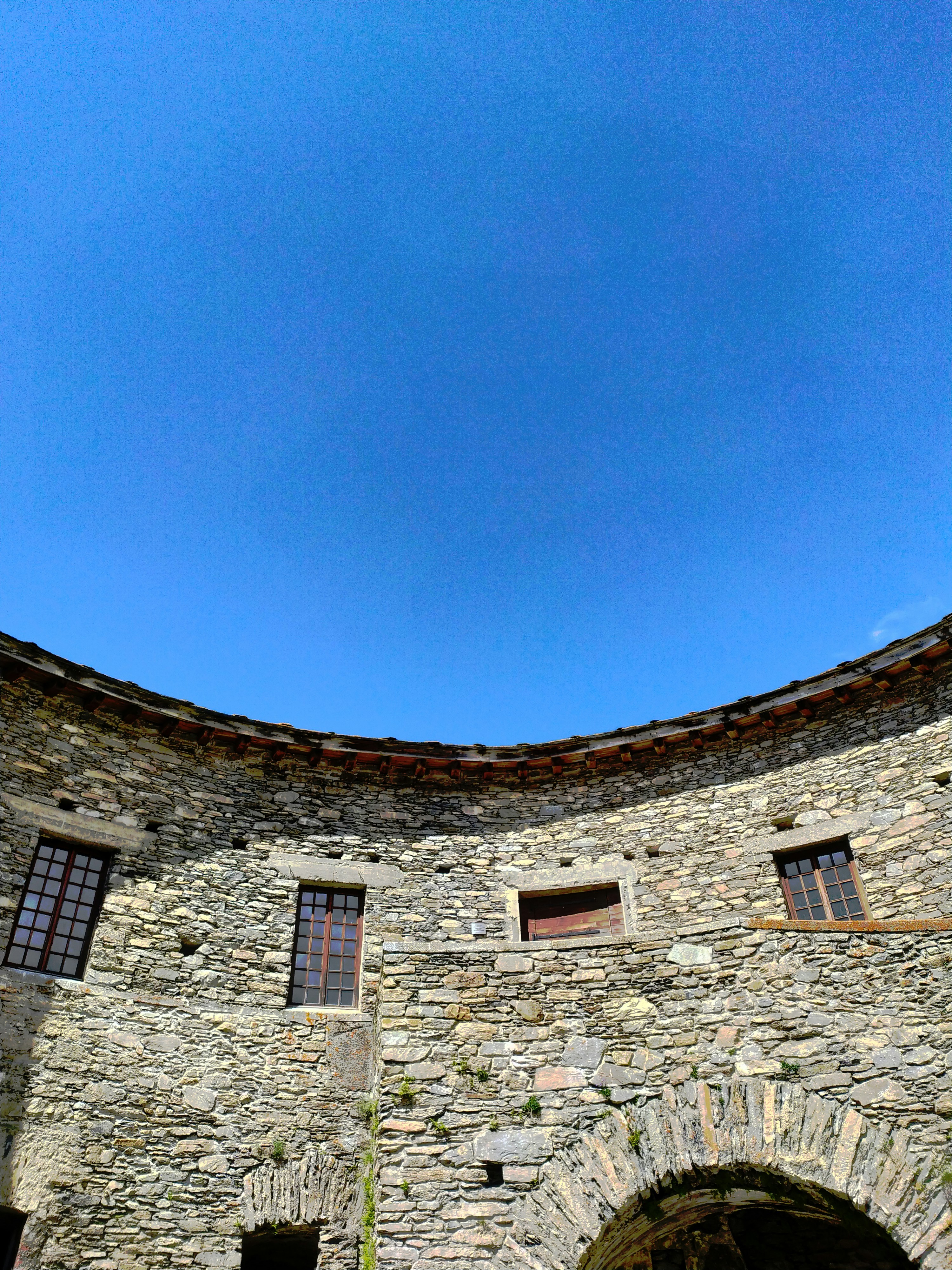 Arched Echoes: Stone Courtyard Framed by a Vast Blue Sky