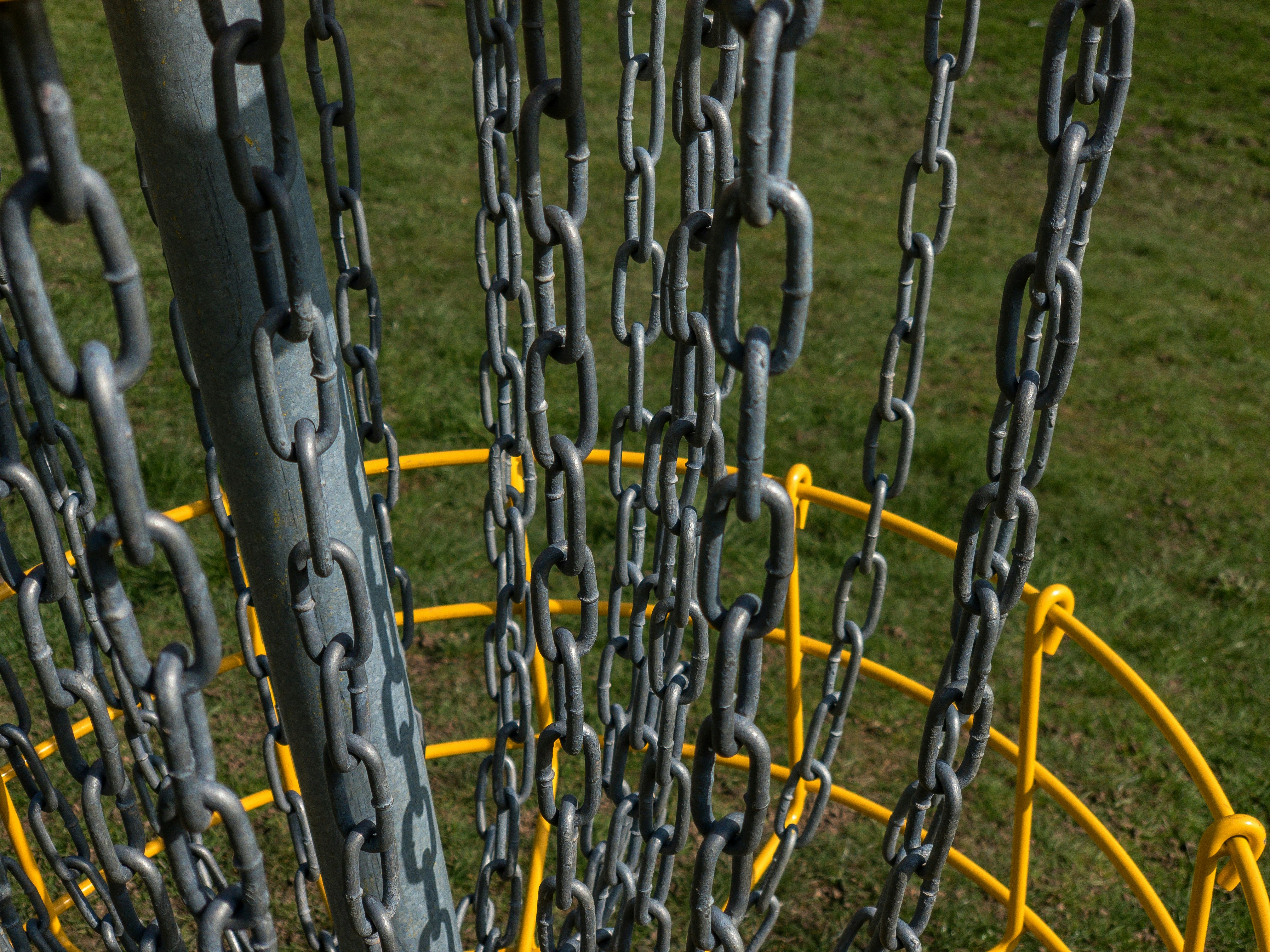 Close-up view of a disc golf basket's chains and metal frame, showcasing the intricate design and functionality. The vibrant yellow rim contrasts with the metallic chains.