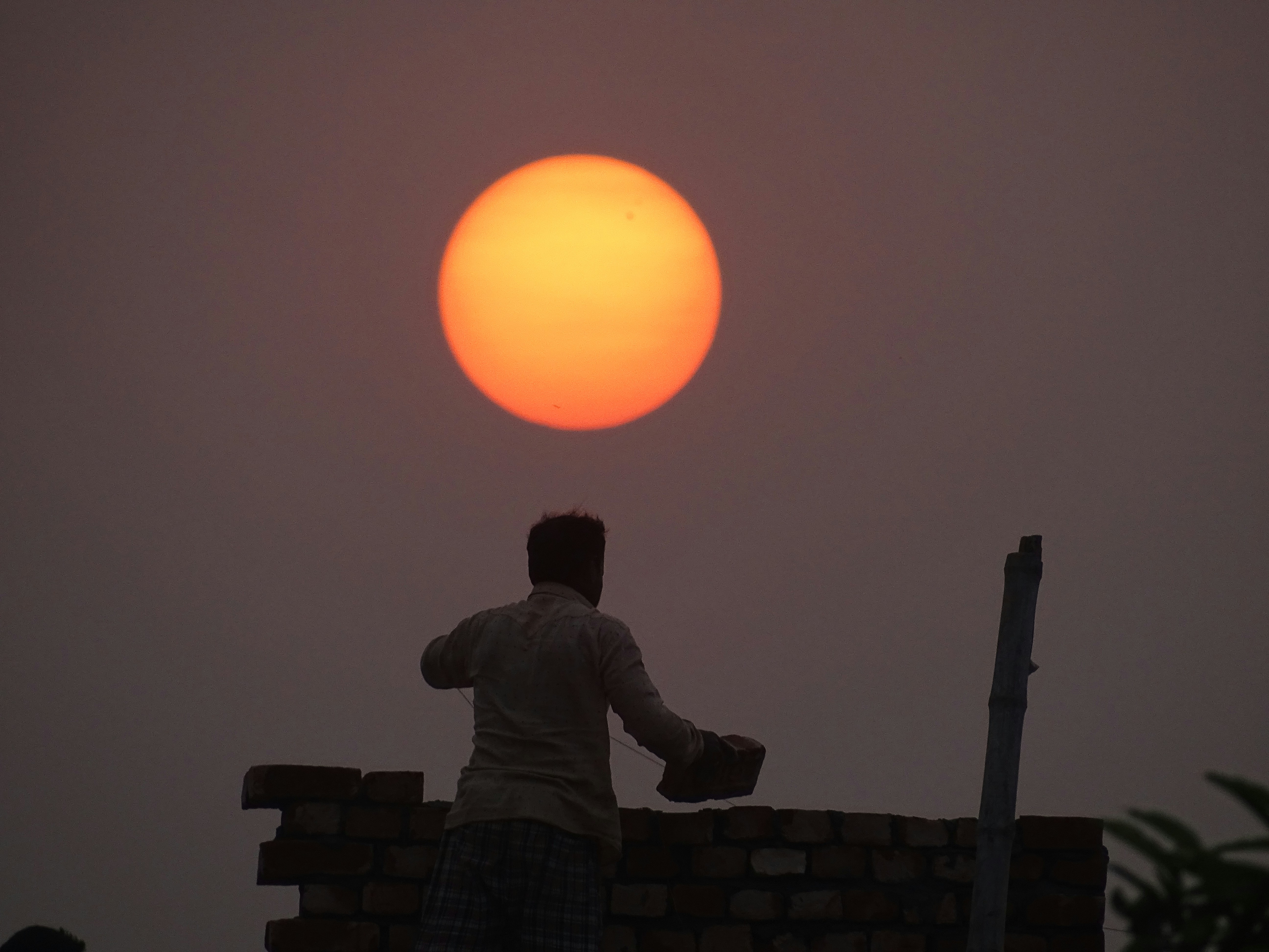 Silhouette of a laborer stacking bricks against a vibrant sunset backdrop, illustrating the intersection of human effort and nature's beauty.