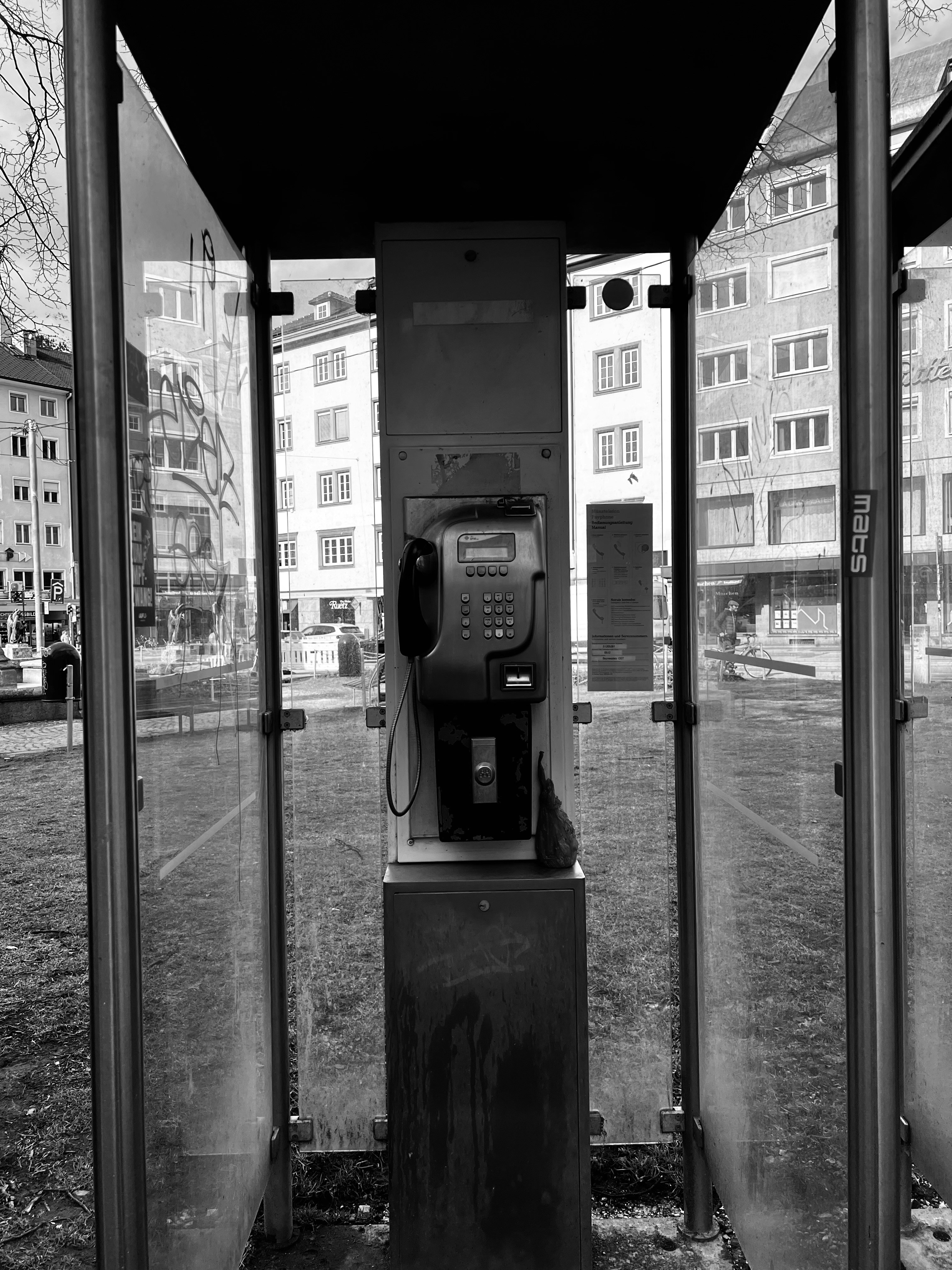 Grayscale Gateway: The Glass-Fronted Payphone in a Quiet Street