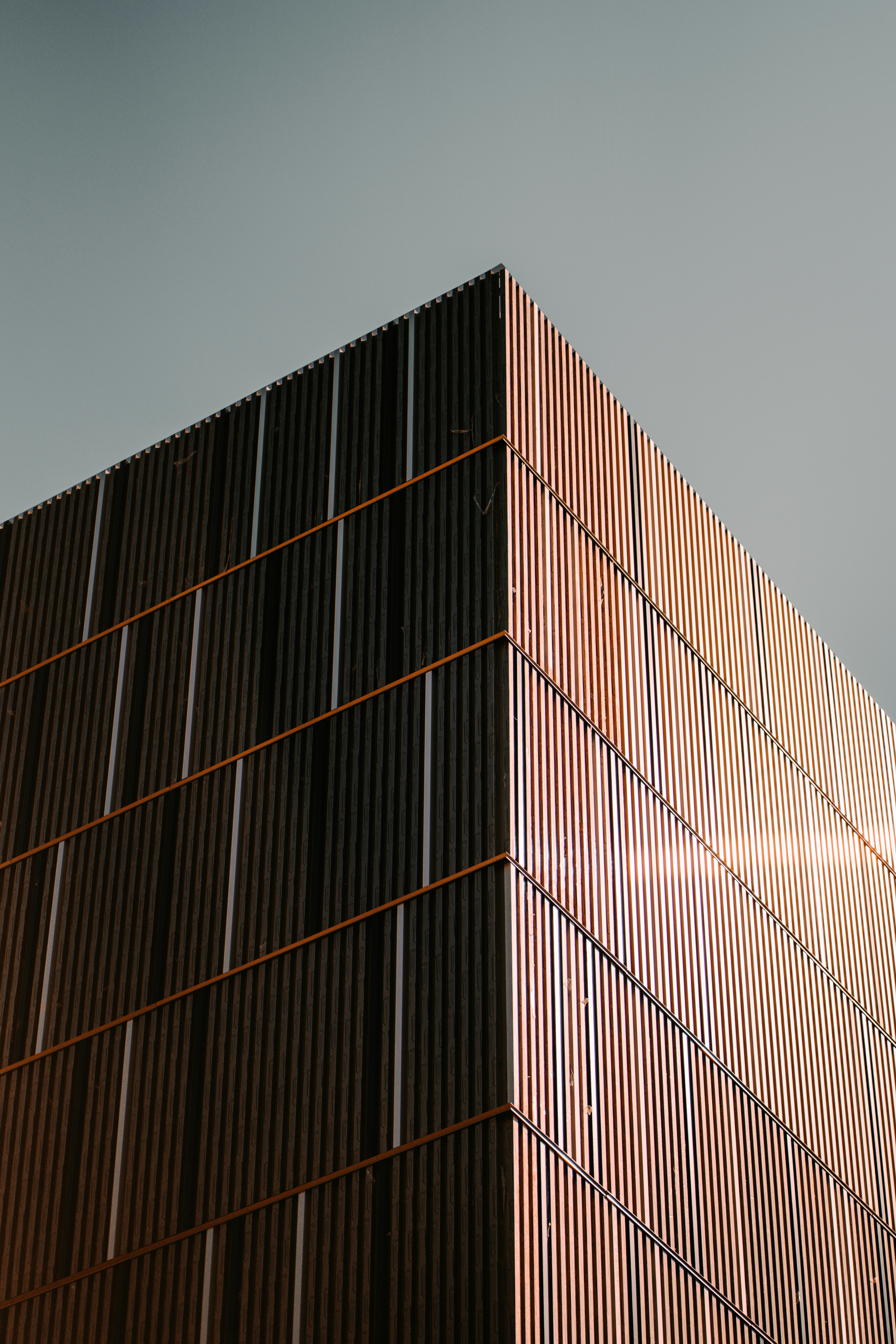 Angular view of a modern building showcasing its textured facade and interplay of light and shadow. The design emphasizes vertical lines and contrasting colors.