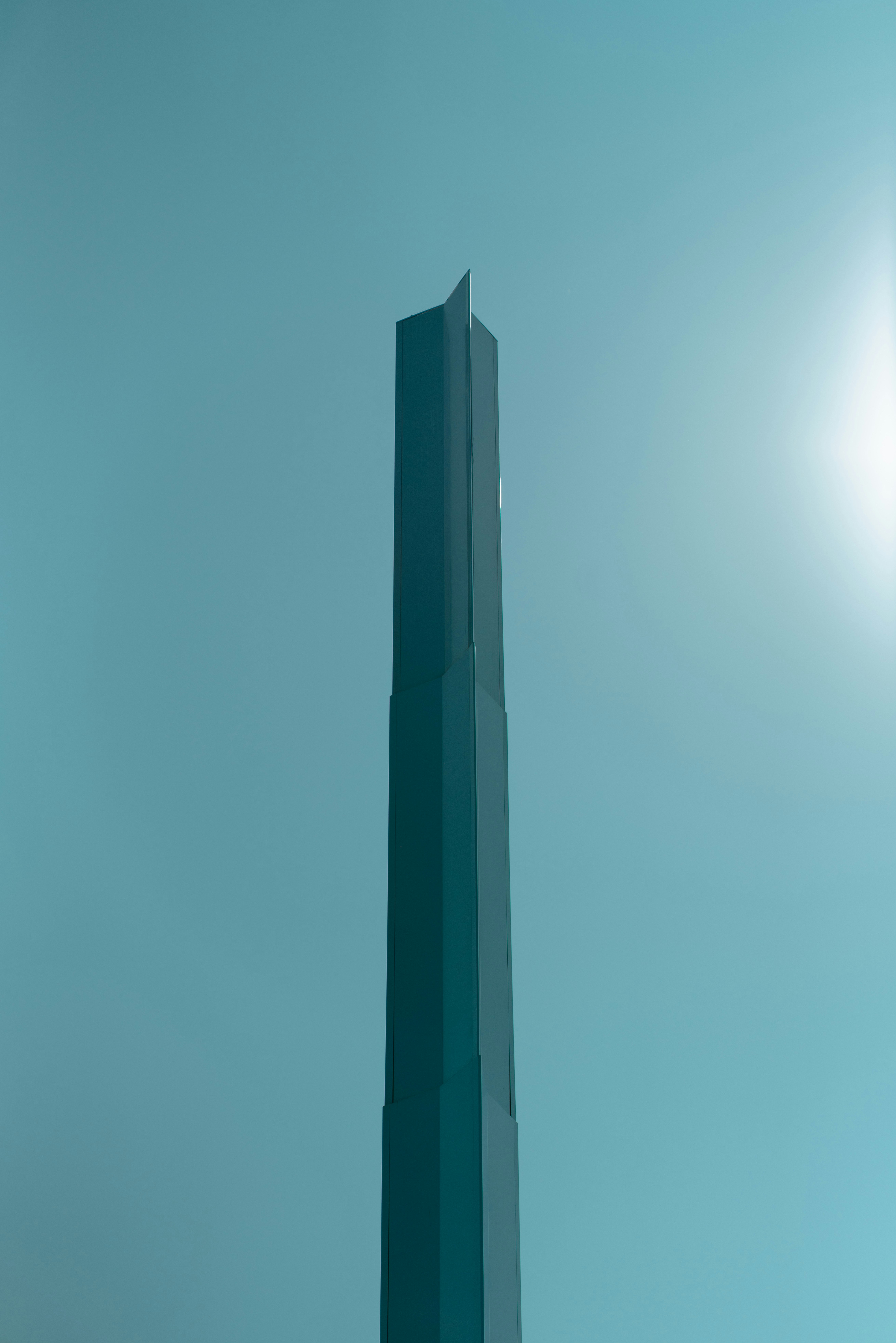 Sleek, modern tower reaching towards a clear sky, illuminated by sunlight. The structure's sharp lines and reflective surfaces create a striking silhouette.