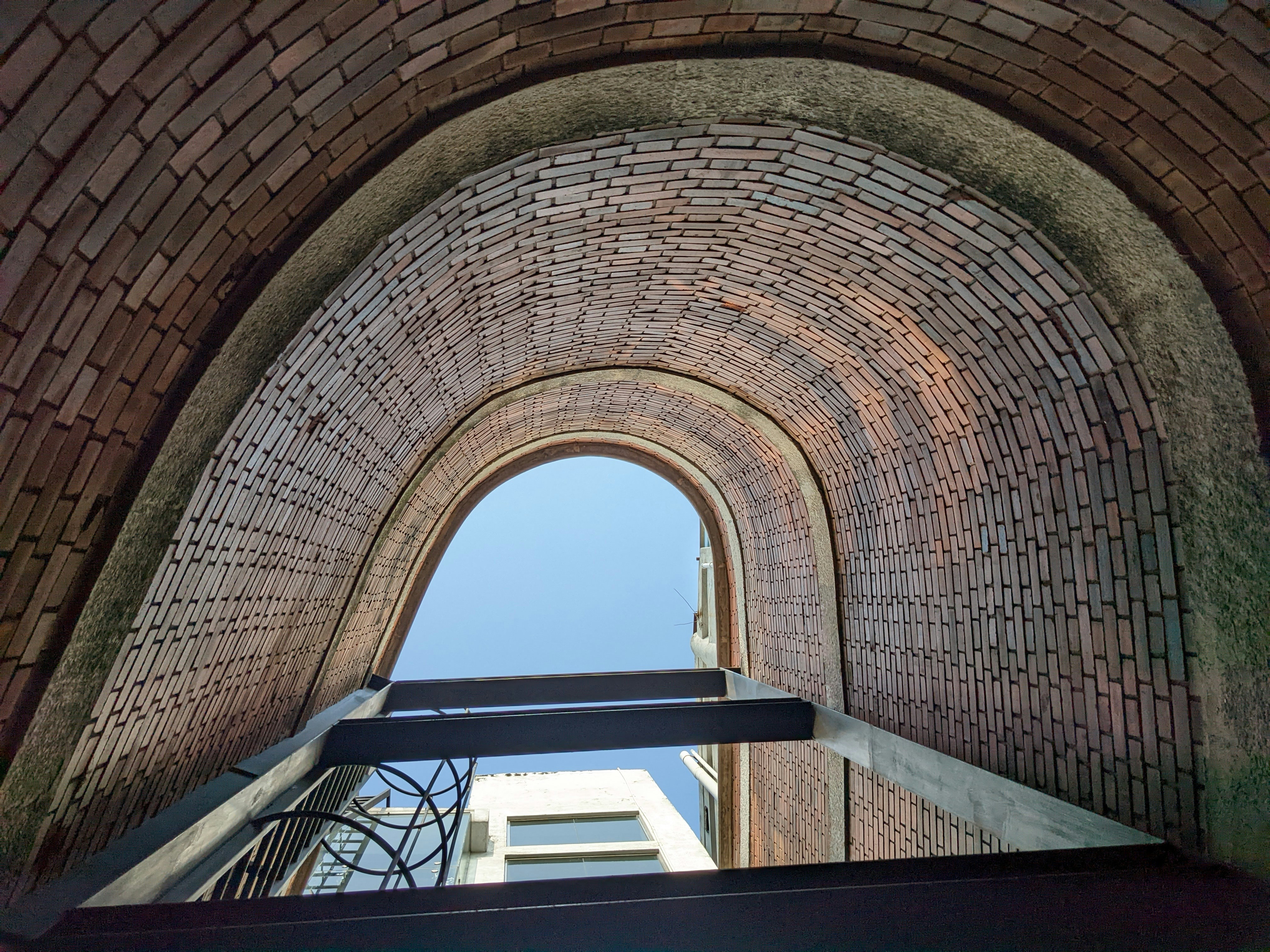 Brick archway frames a clear blue sky, with modern building elements visible beyond.