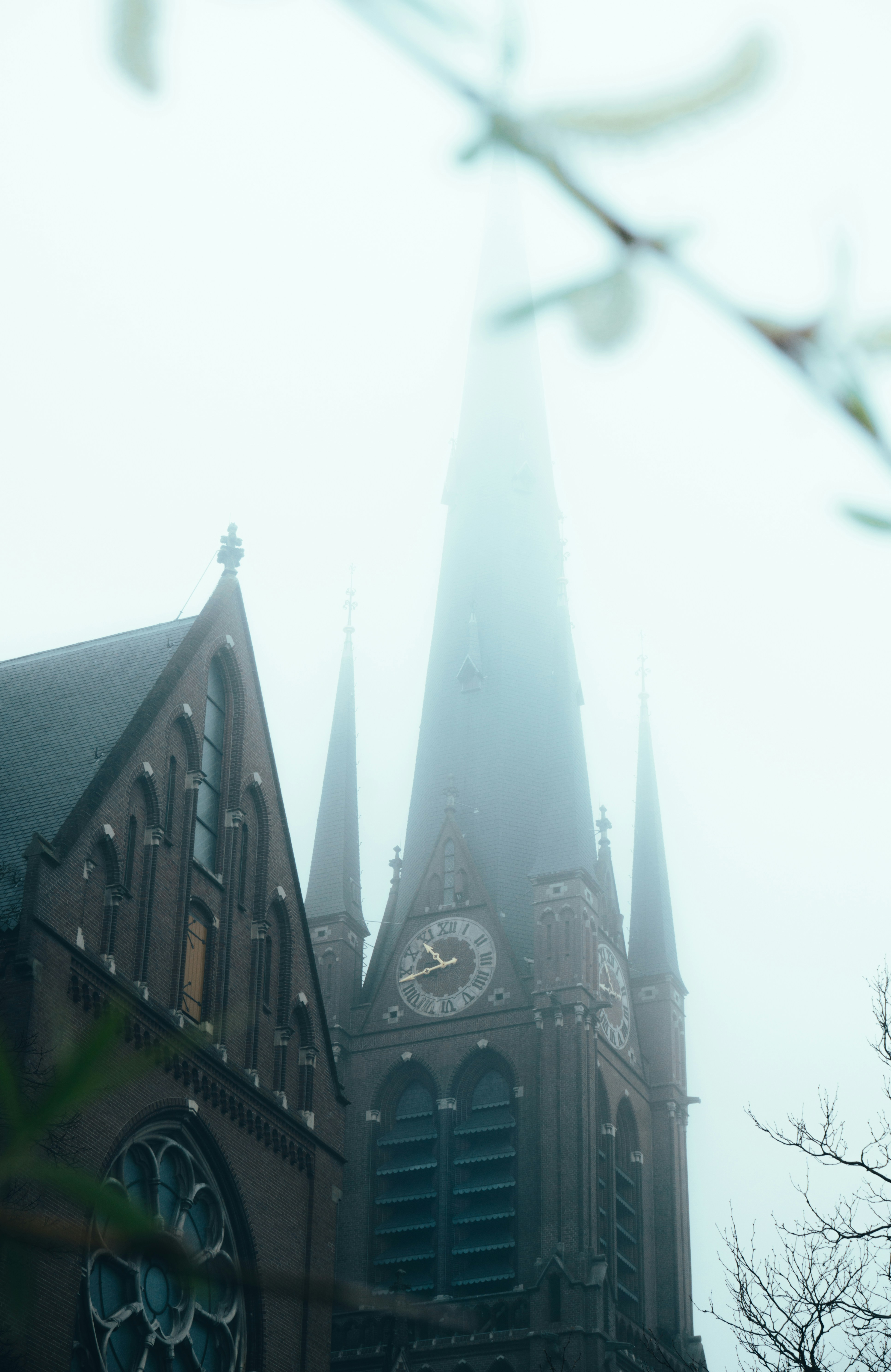 Gothic church tower partially obscured by fog, showcasing intricate architecture and a prominent clock face.