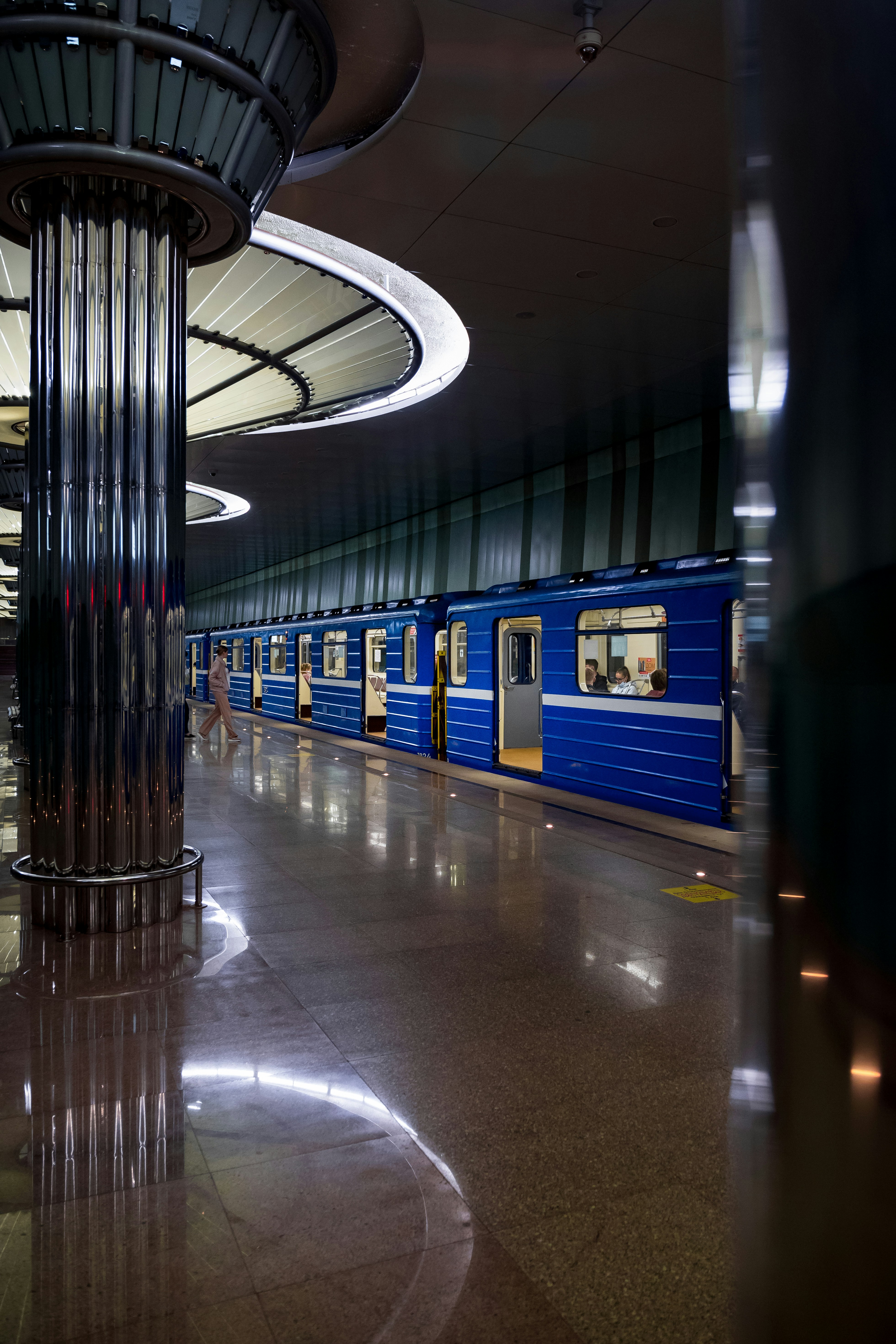 Modern subway station with blue train cars and reflective surfaces under soft lighting.