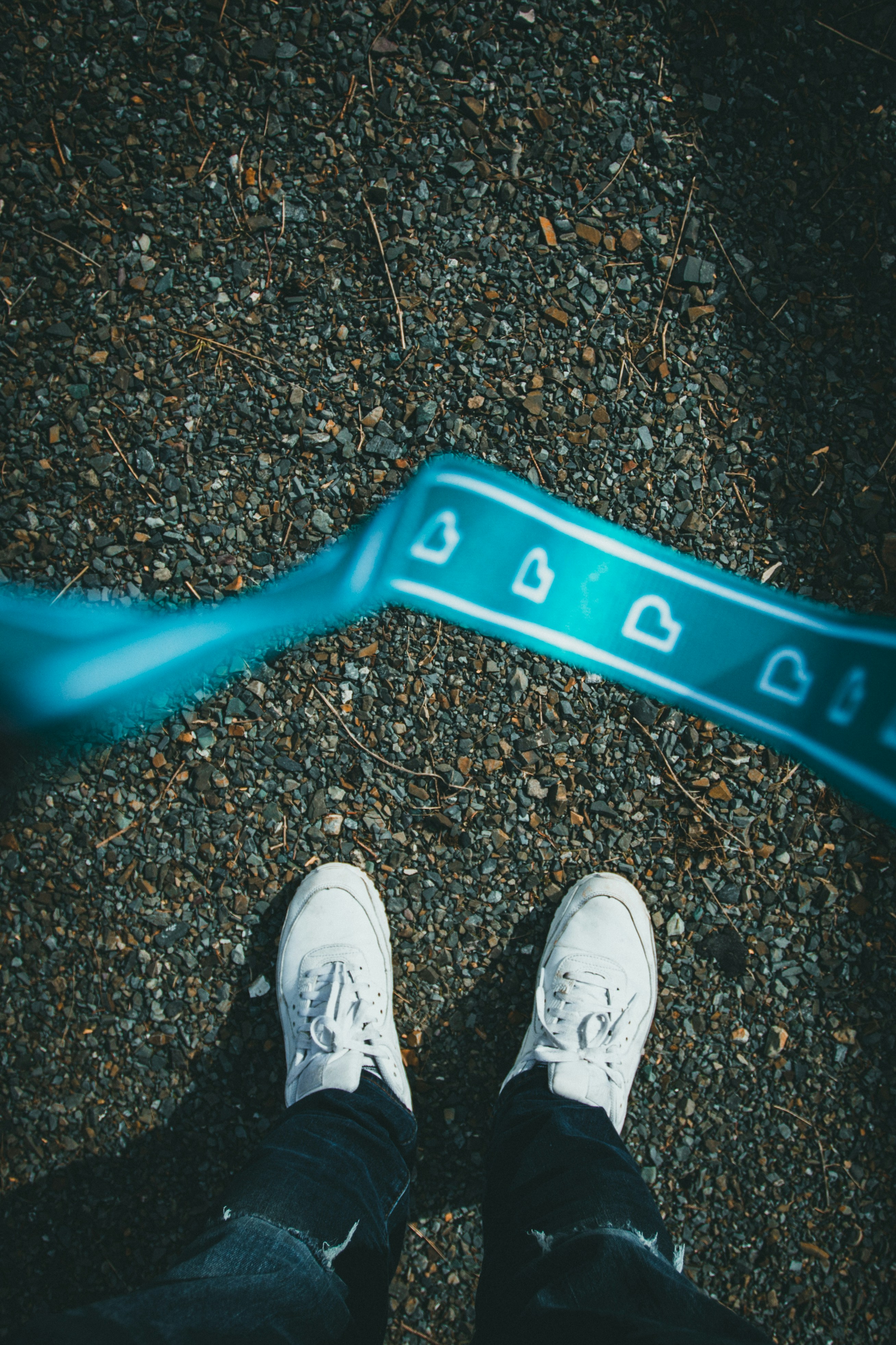Ground-Level Cadence: White Sneakers Meet a Neon Blue Tape Across Gravel