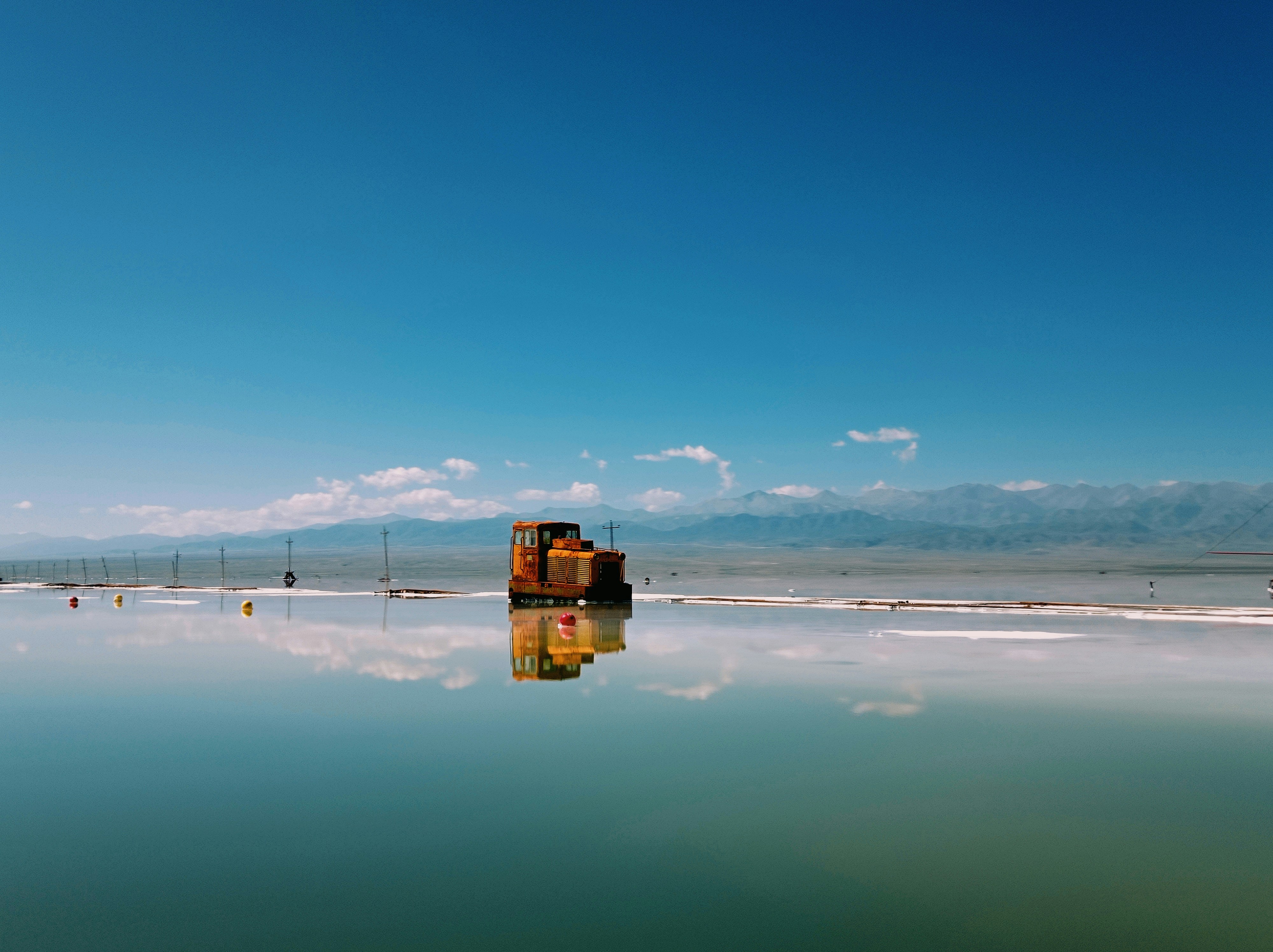 Rusty yellow tugboat reflected in calm, expansive lake under a clear blue sky.