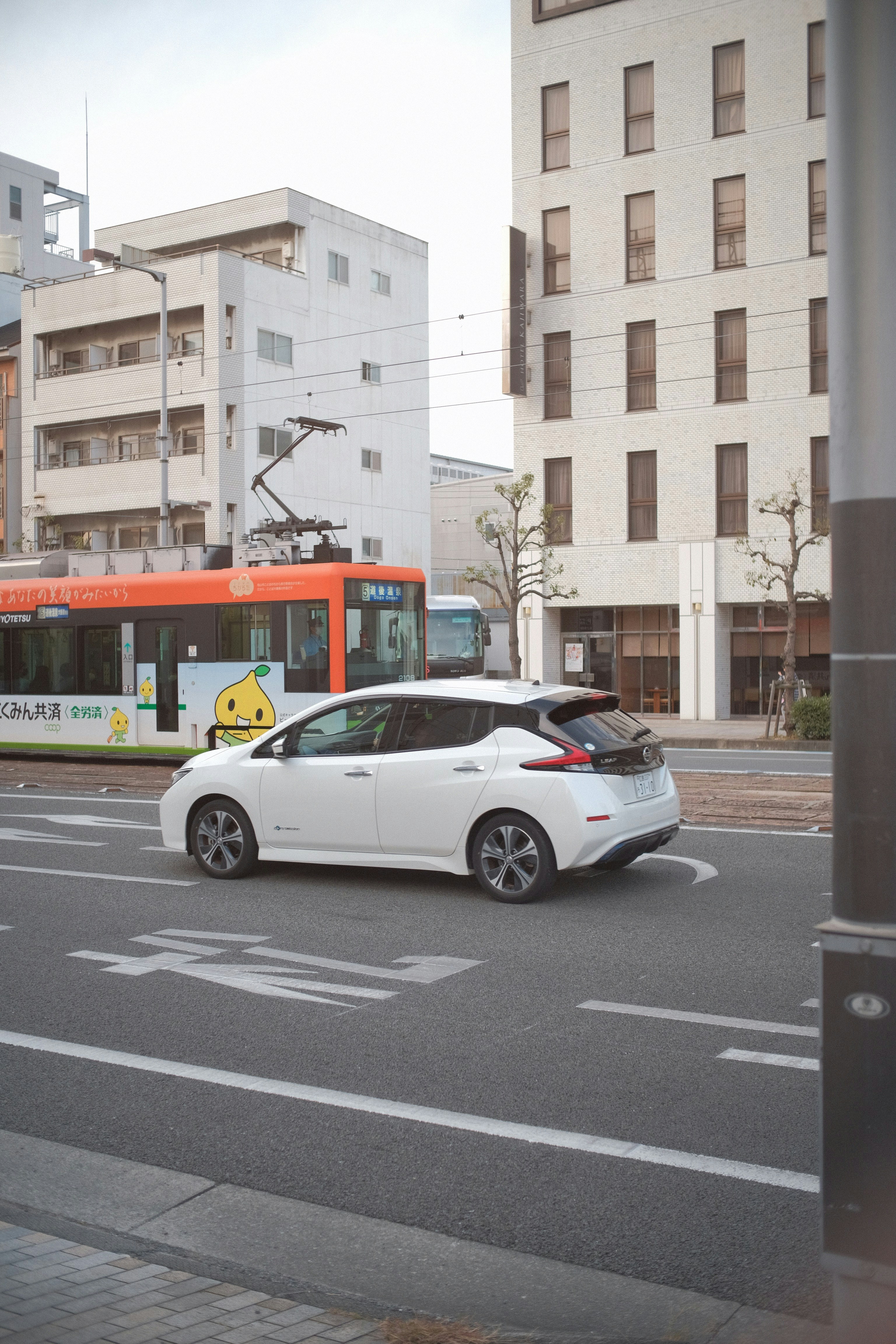 A white car driving down a street next to a bus photo – Free Car Image ...
