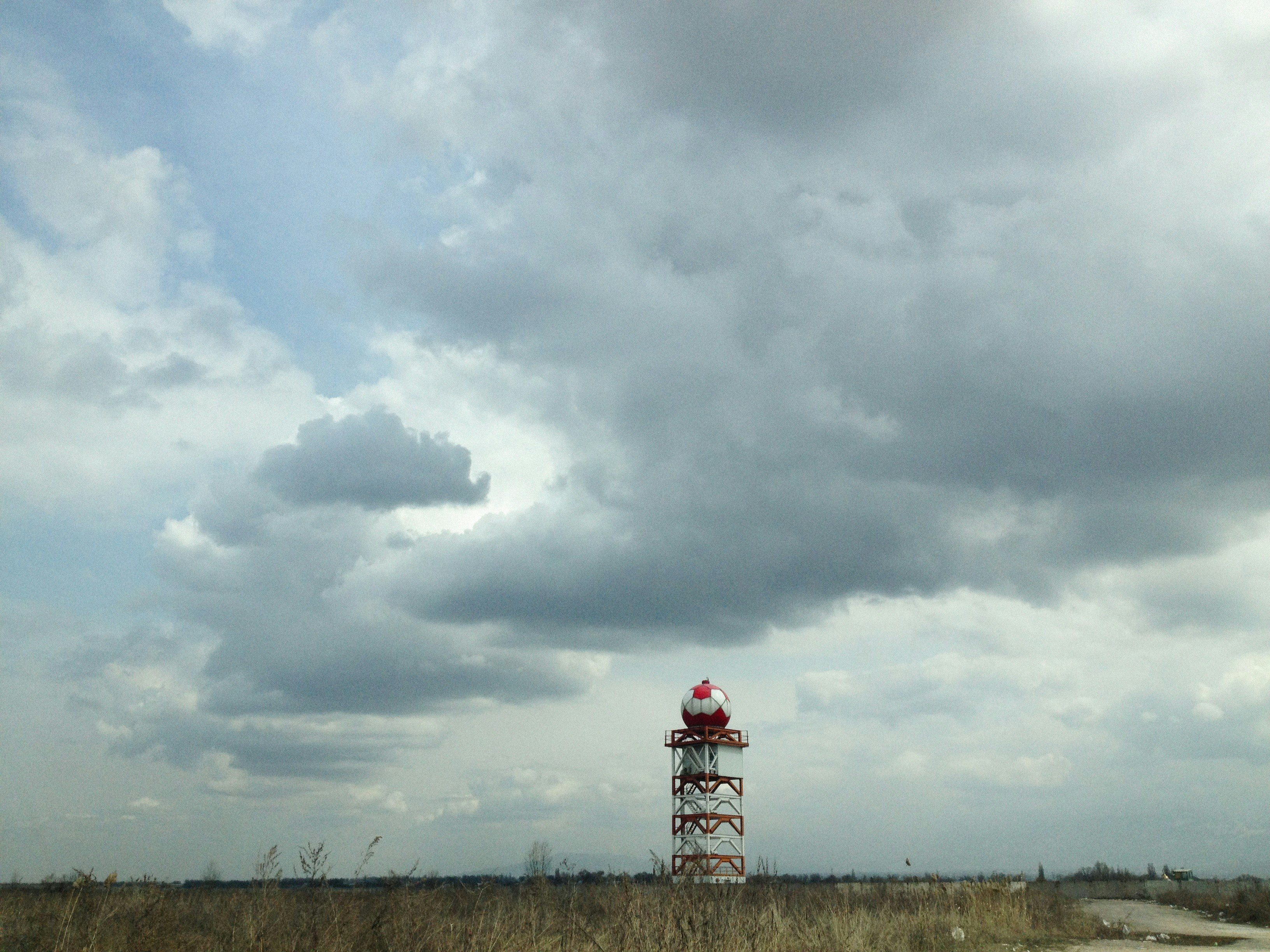 Red Lattice Beacon on the Plain: a Quiet Sentinel Under Moody Skies