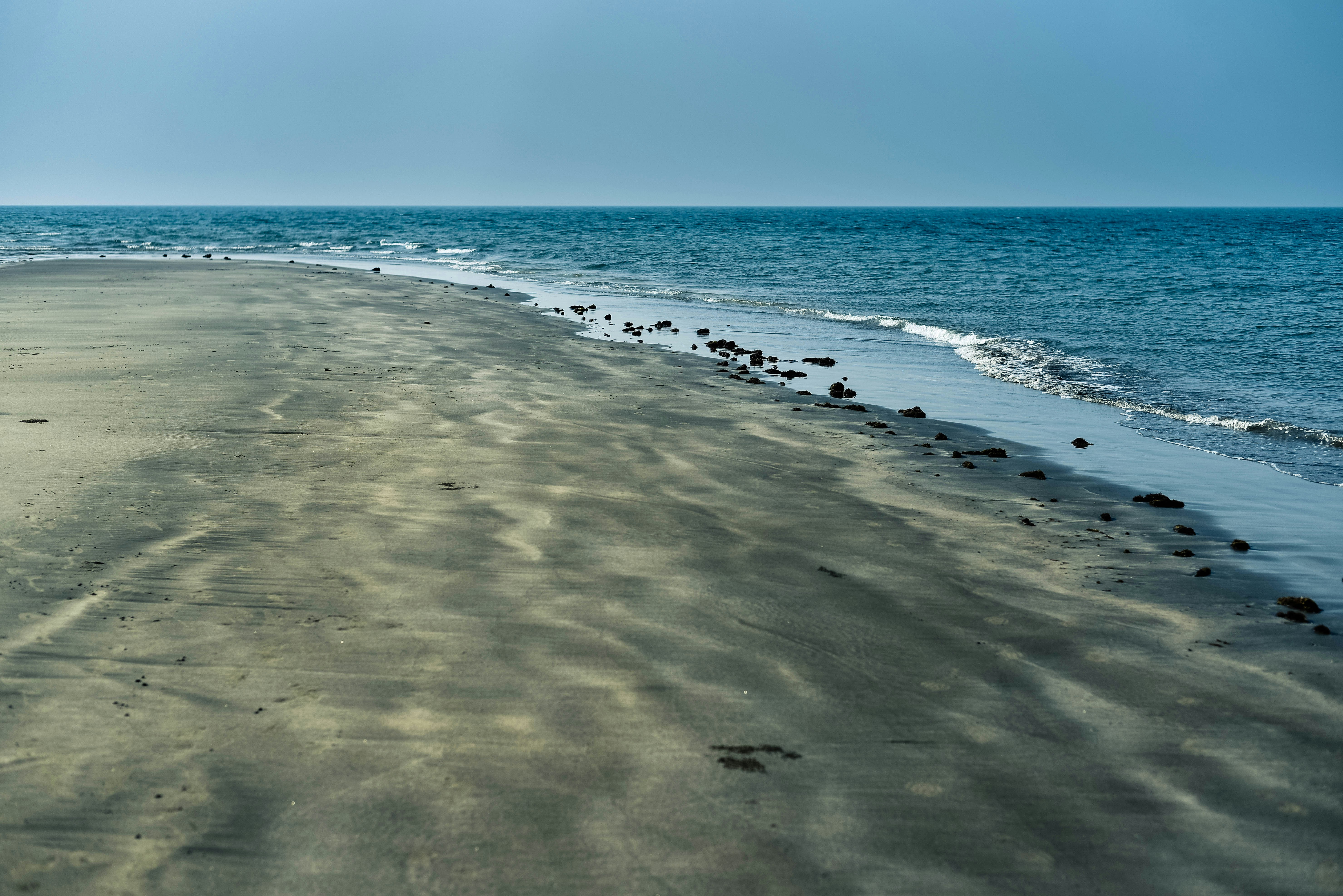 Sandy shoreline gently curving into the ocean, with scattered stones and soft waves lapping at the beach. The atmosphere exudes tranquility.