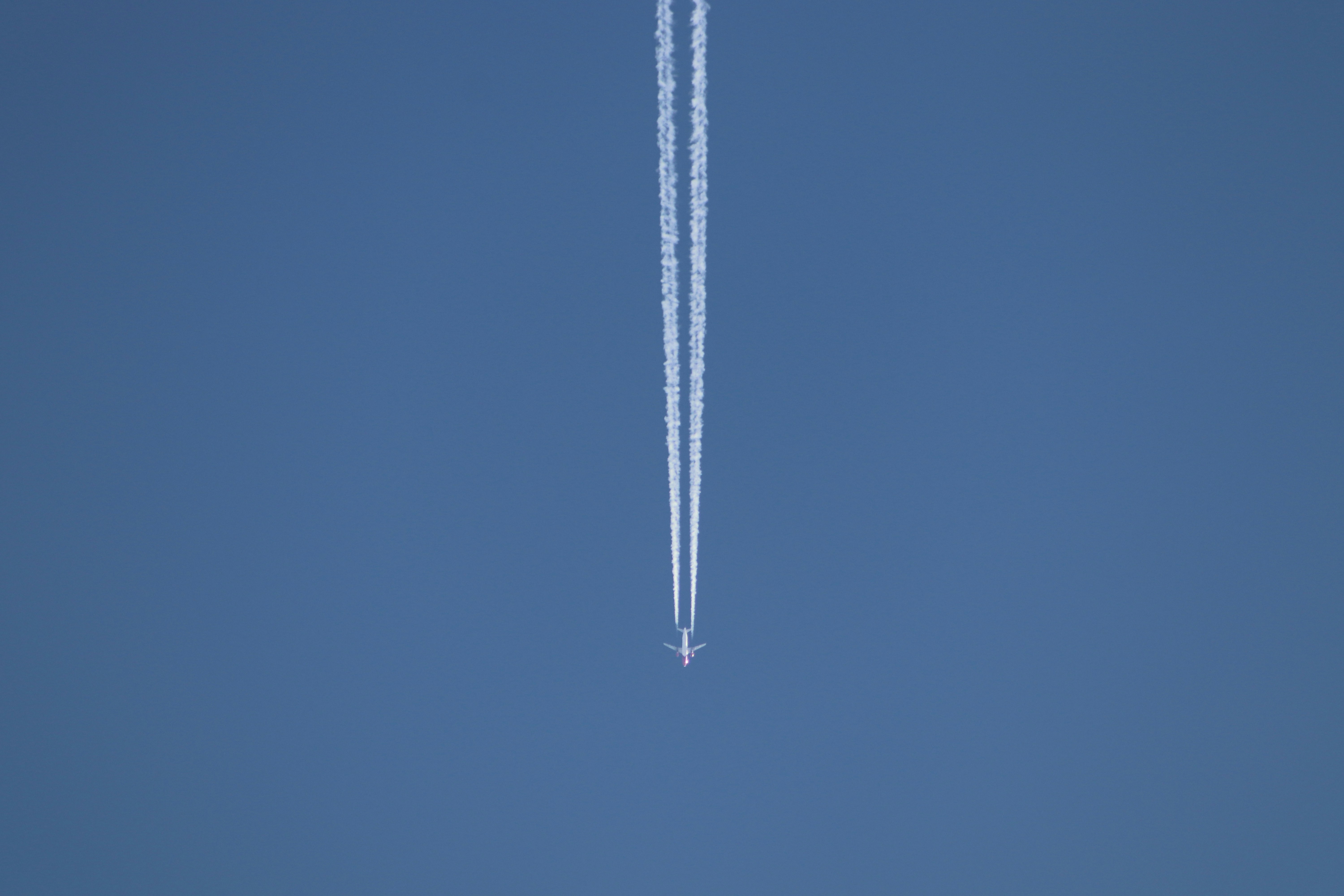 Airplane leaving a vapor trail against a clear blue sky, showcasing the contrast between man-made flight and nature's expanse.