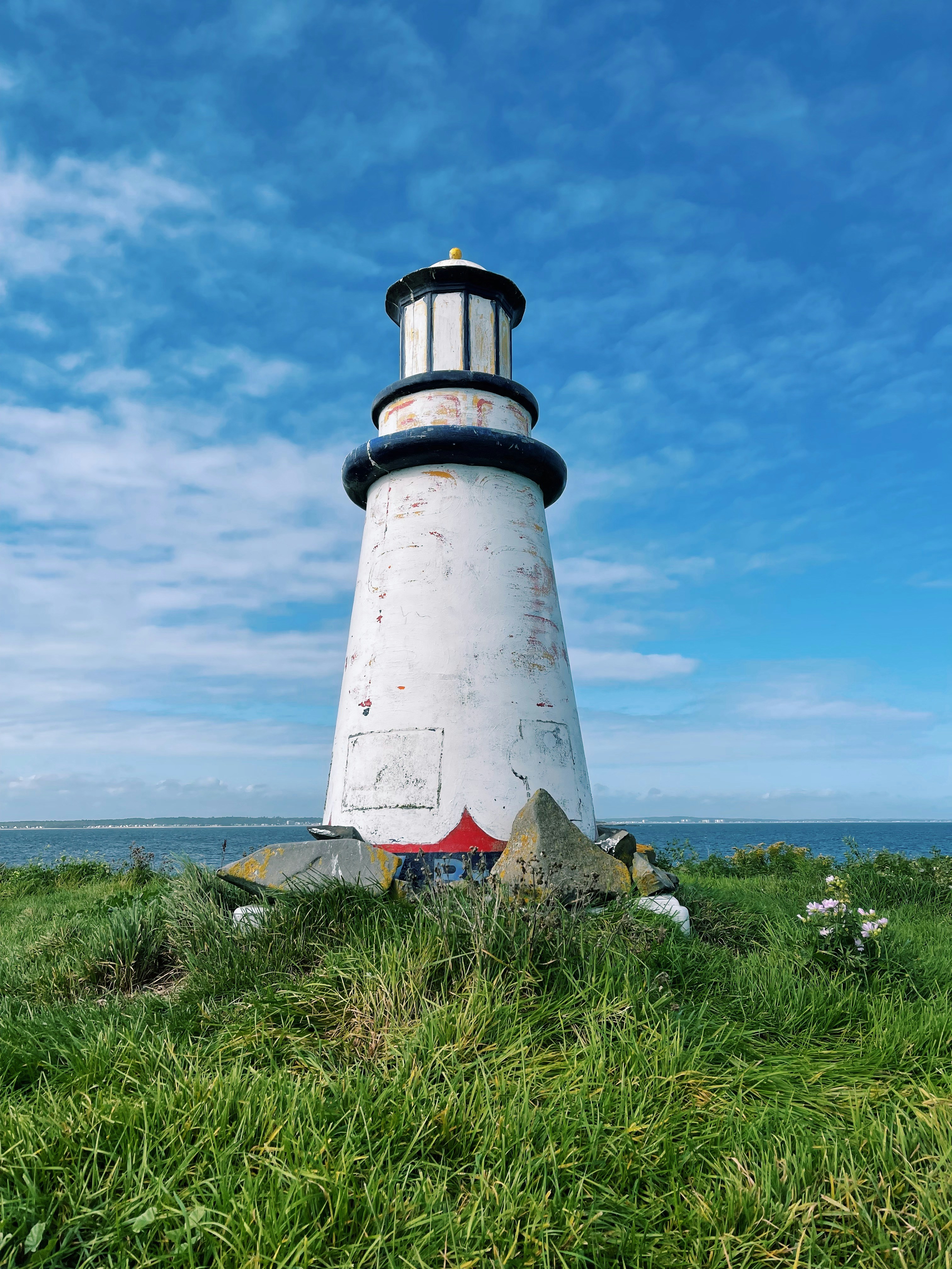 White lighthouse standing tall amid lush green grass against a vibrant blue sky.