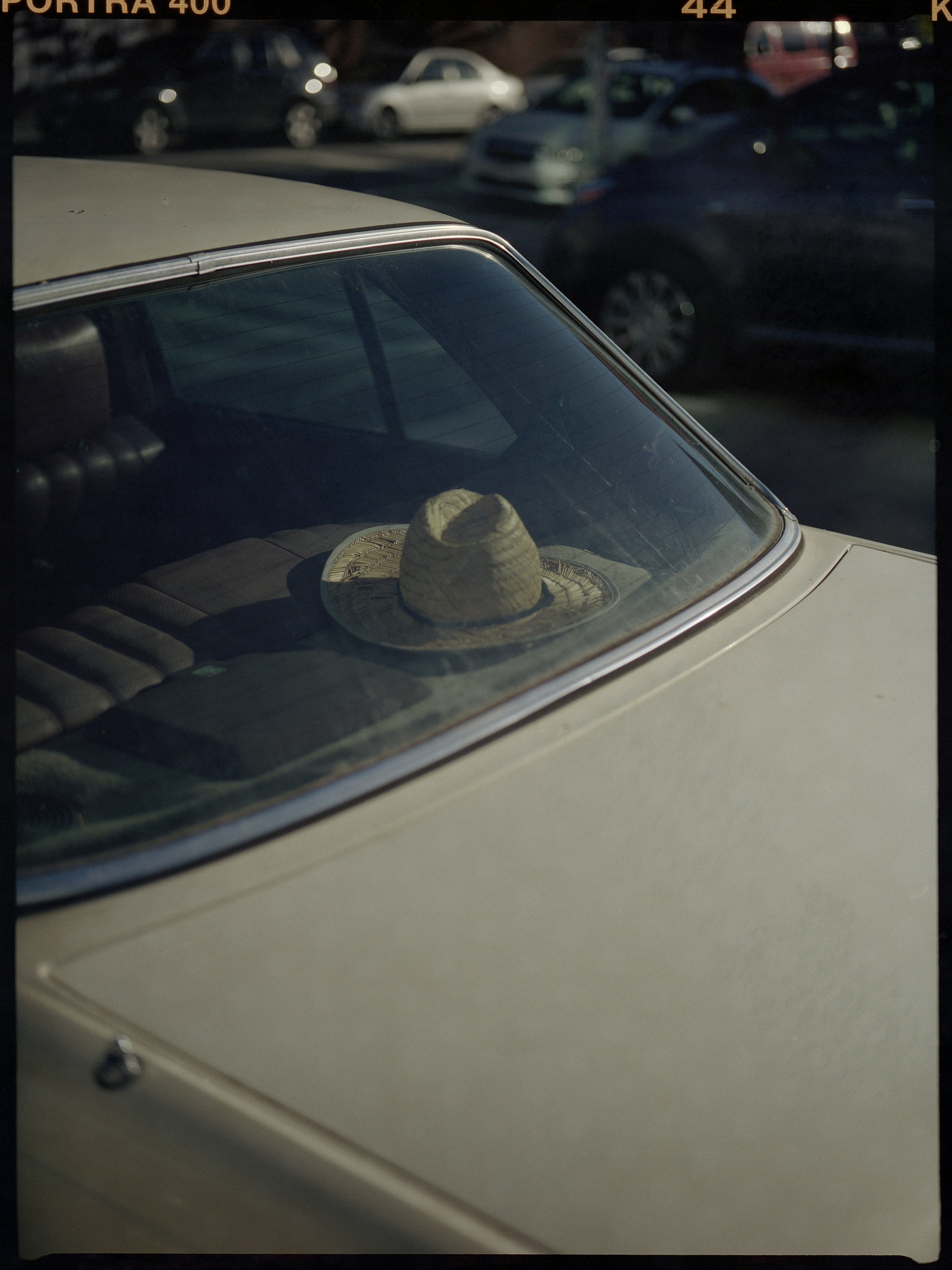 Straw hat resting on the back seat of a classic car, viewed through the rear window, capturing a sense of nostalgia and stillness.