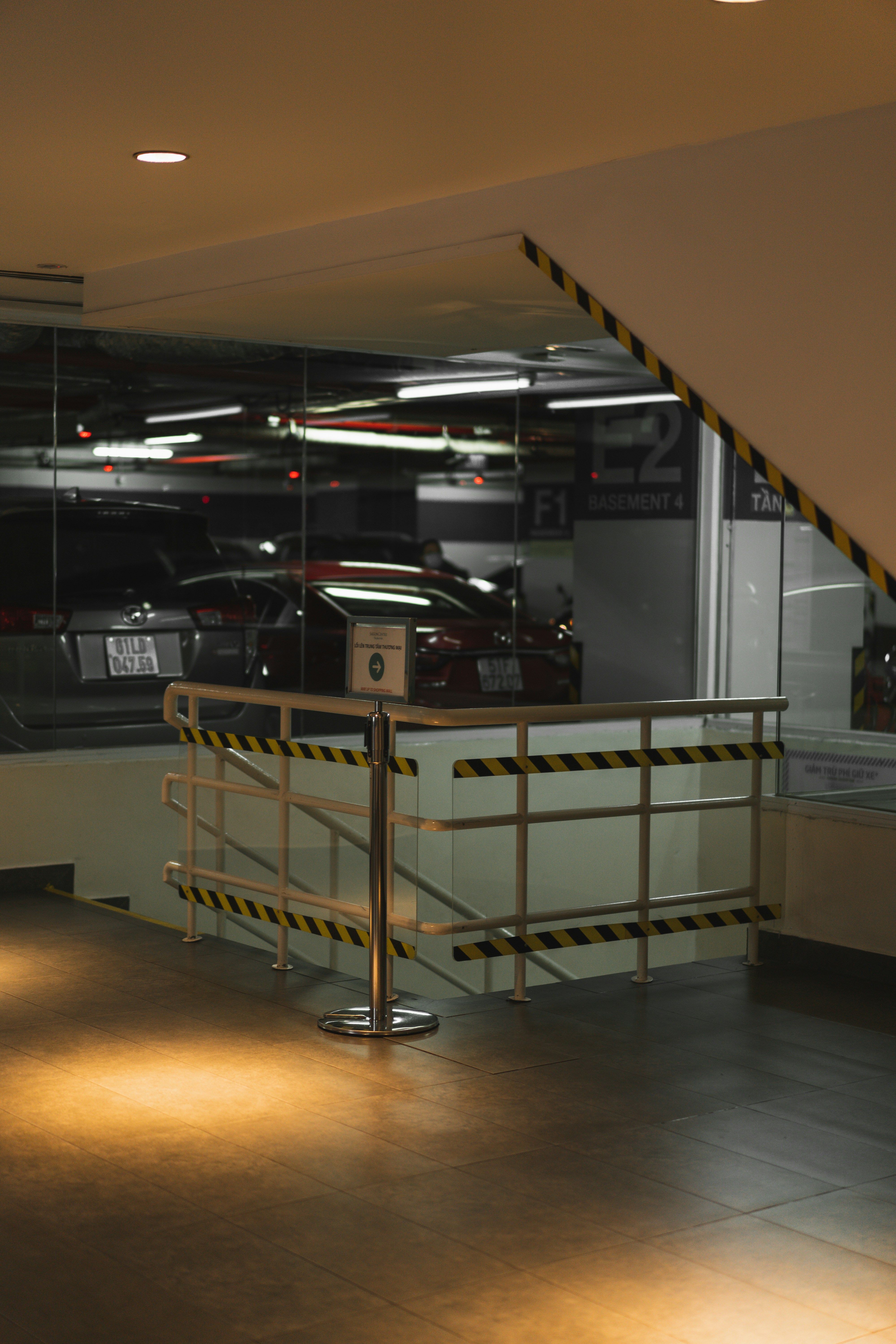 A well-lit parking garage entrance featuring a railing and directional signage, with parked cars visible through glass walls.