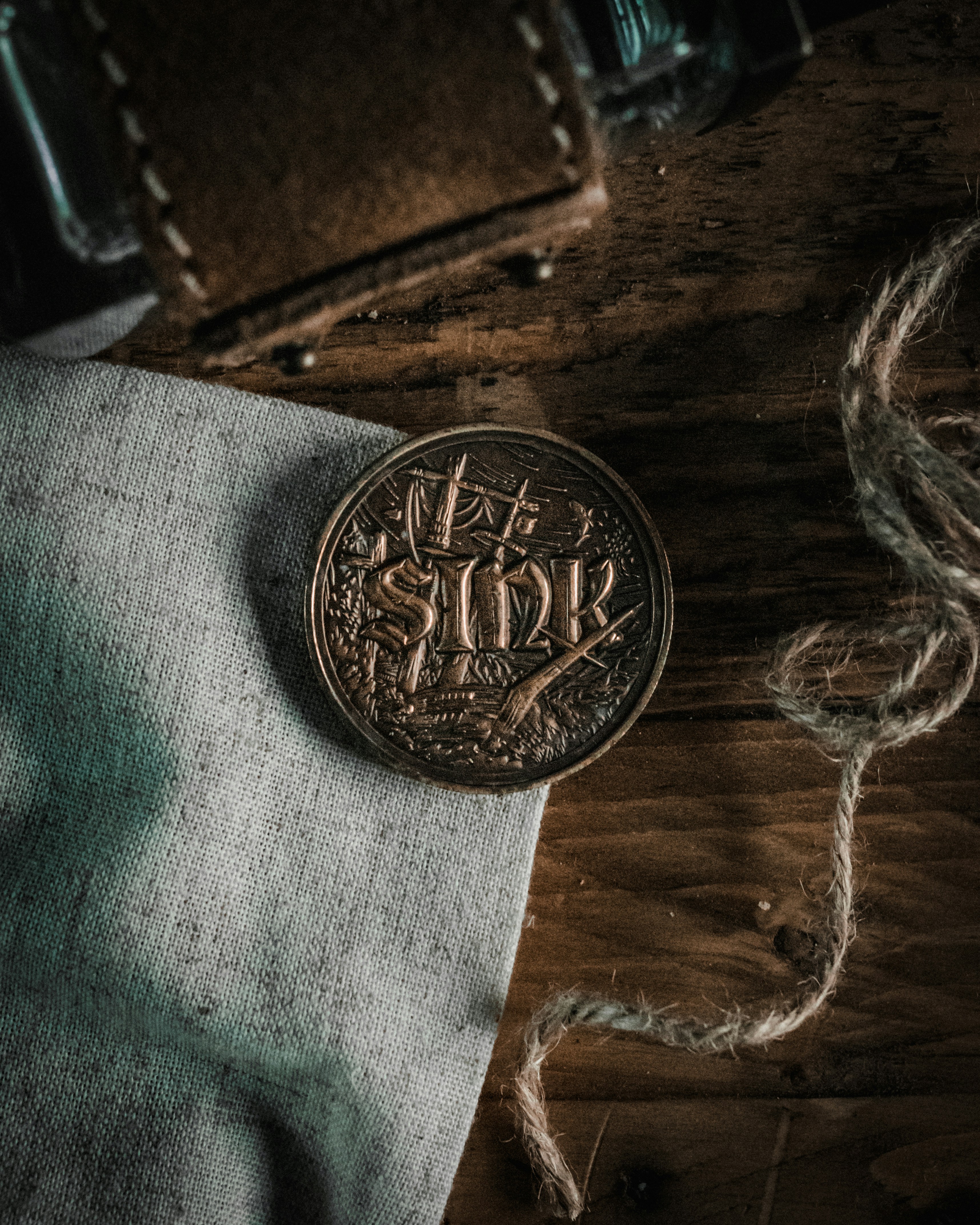 Antique coin with the word 'SINK' etched prominently, resting on a textured fabric with a rustic background. 