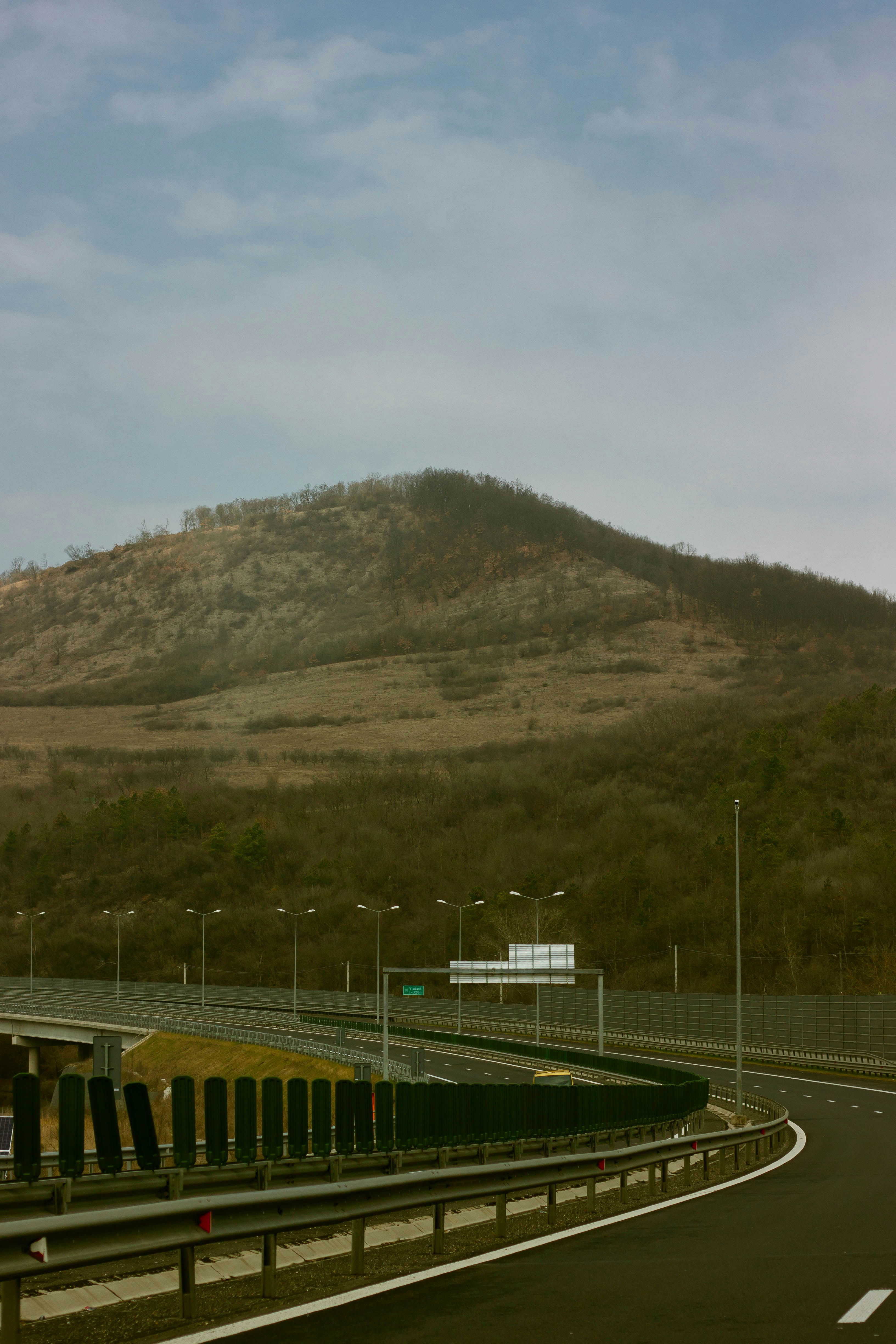 Curving highway leads through a serene landscape dominated by a gently sloping mountain, showcasing the harmony between infrastructure and nature.