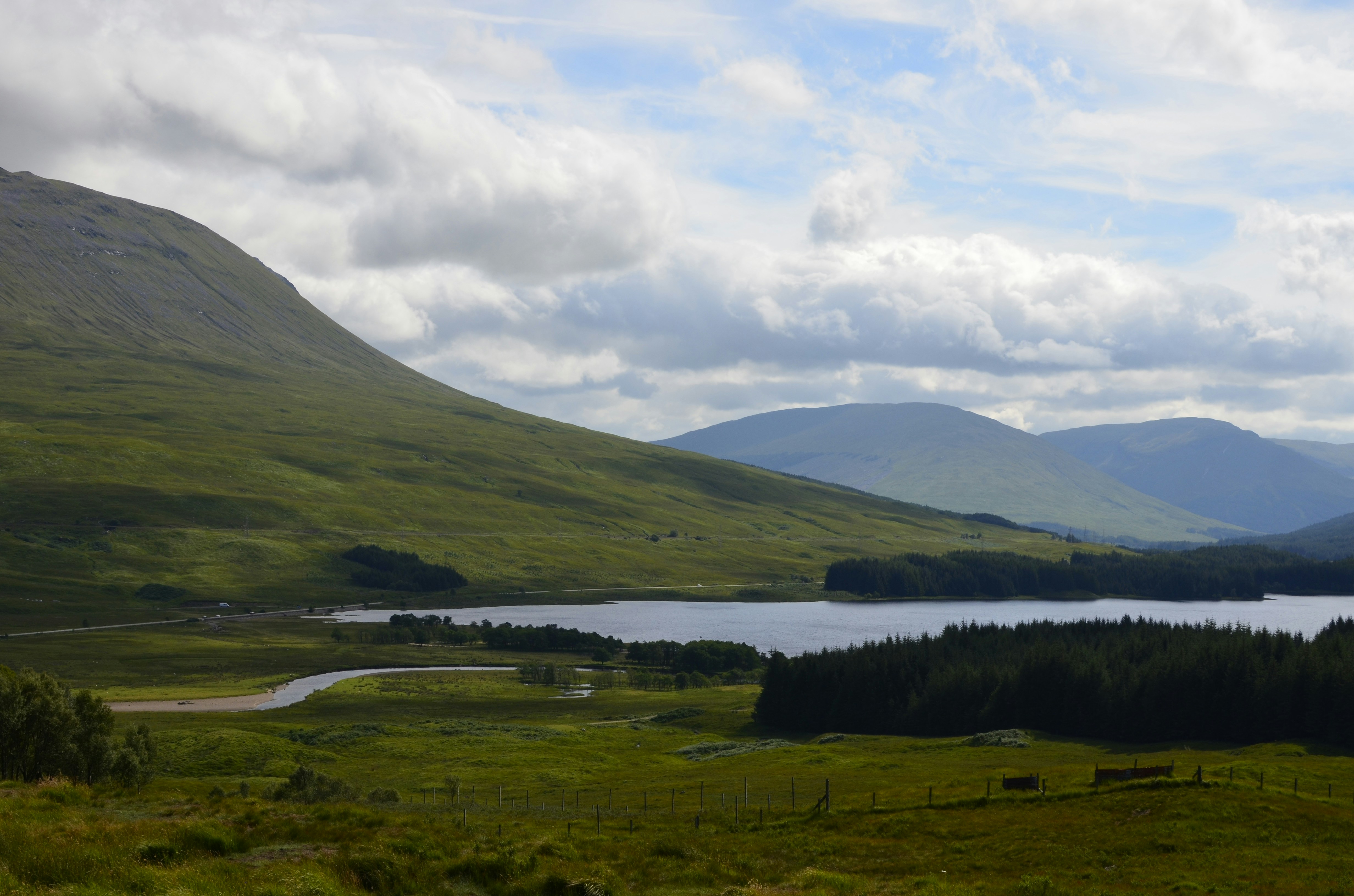 Rolling green hills and a tranquil lake under a cloudy sky.