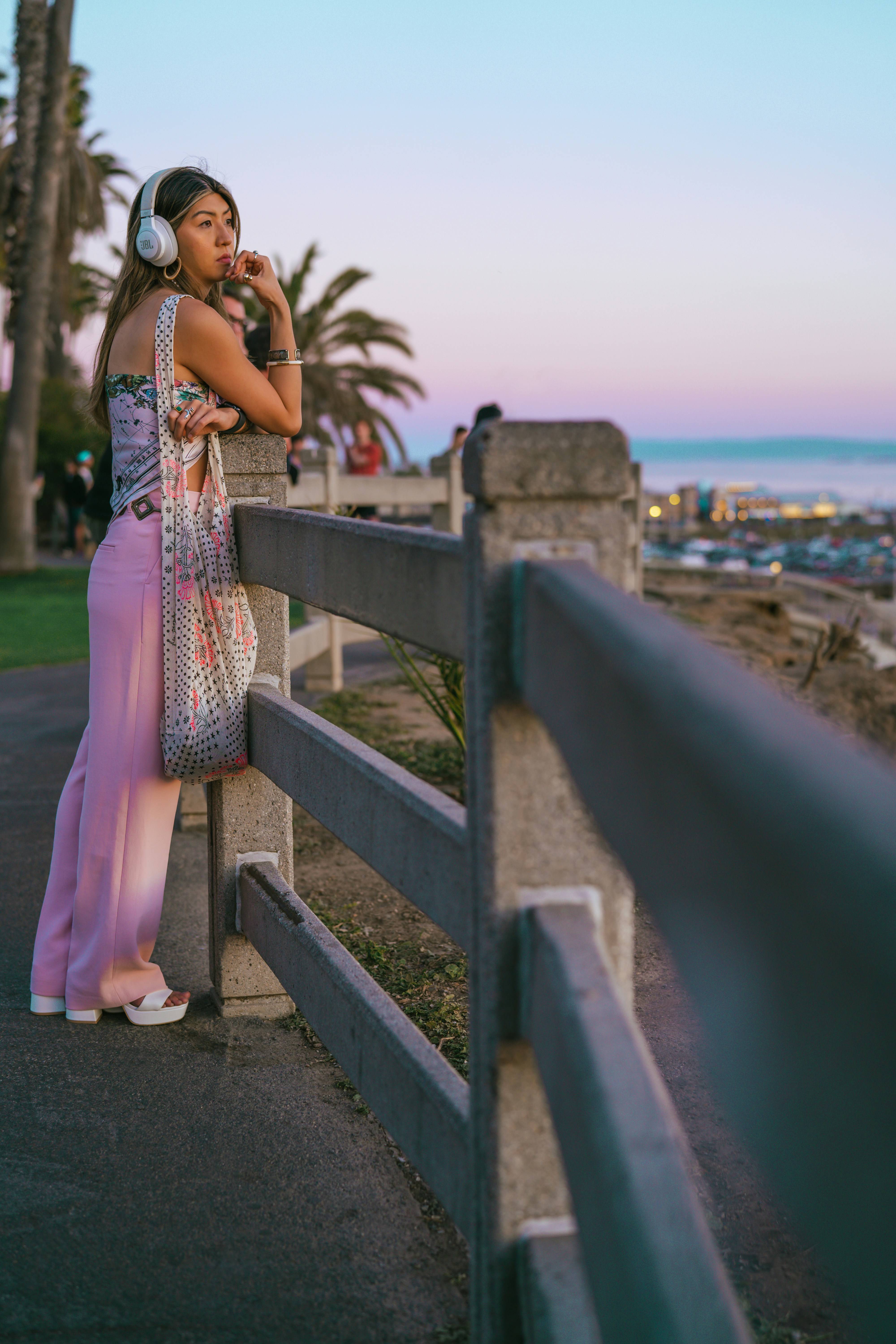 Woman standing next to fence, watching the sun set in Santa Monica, Caifornia.