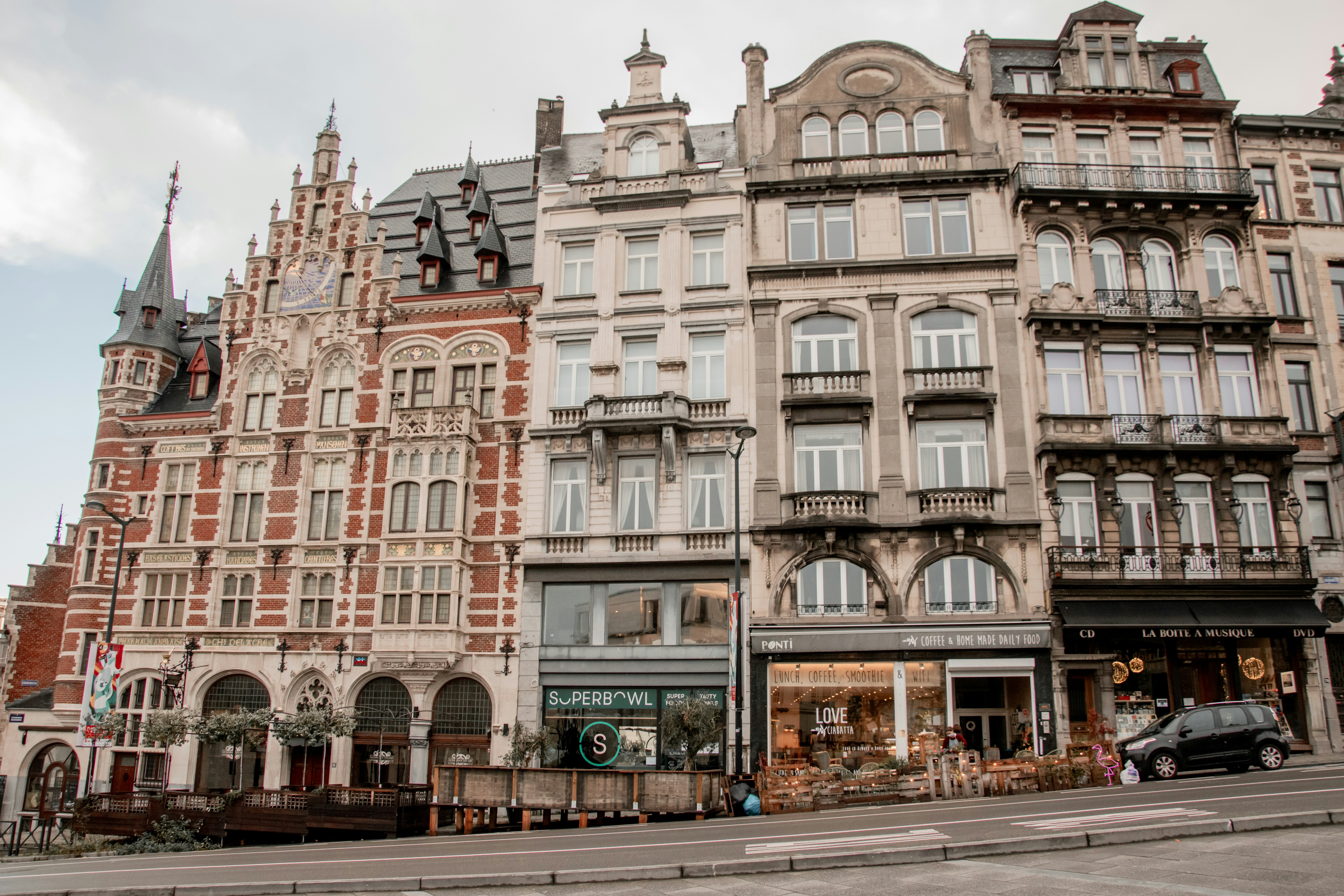 Historic buildings line a charming street, showcasing a blend of intricate facades and modern storefronts. The scene captures the essence of urban life and architectural diversity.