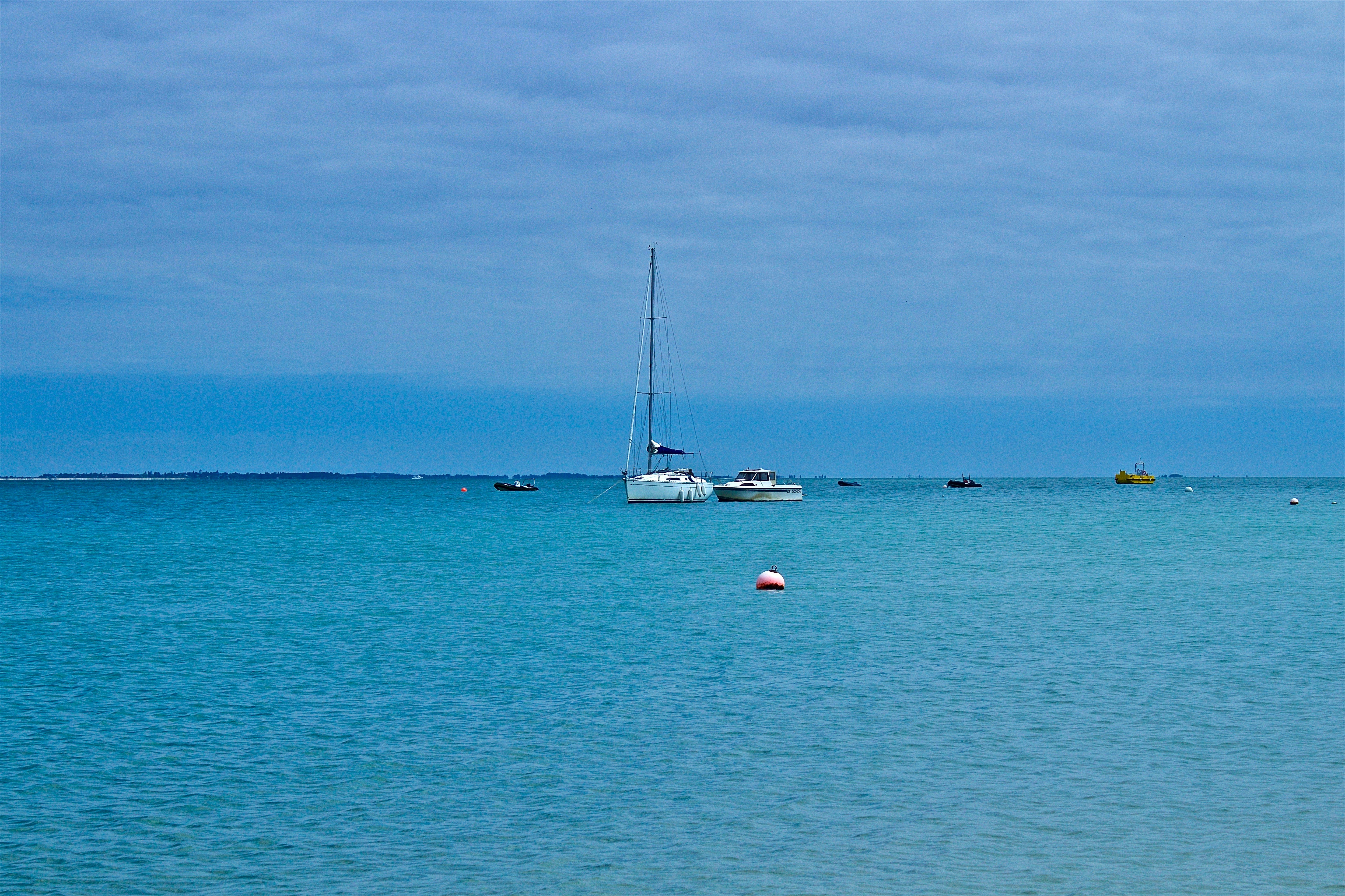 Sailboats anchored in tranquil turquoise waters under a cloudy sky, evoking a sense of calm and leisure.