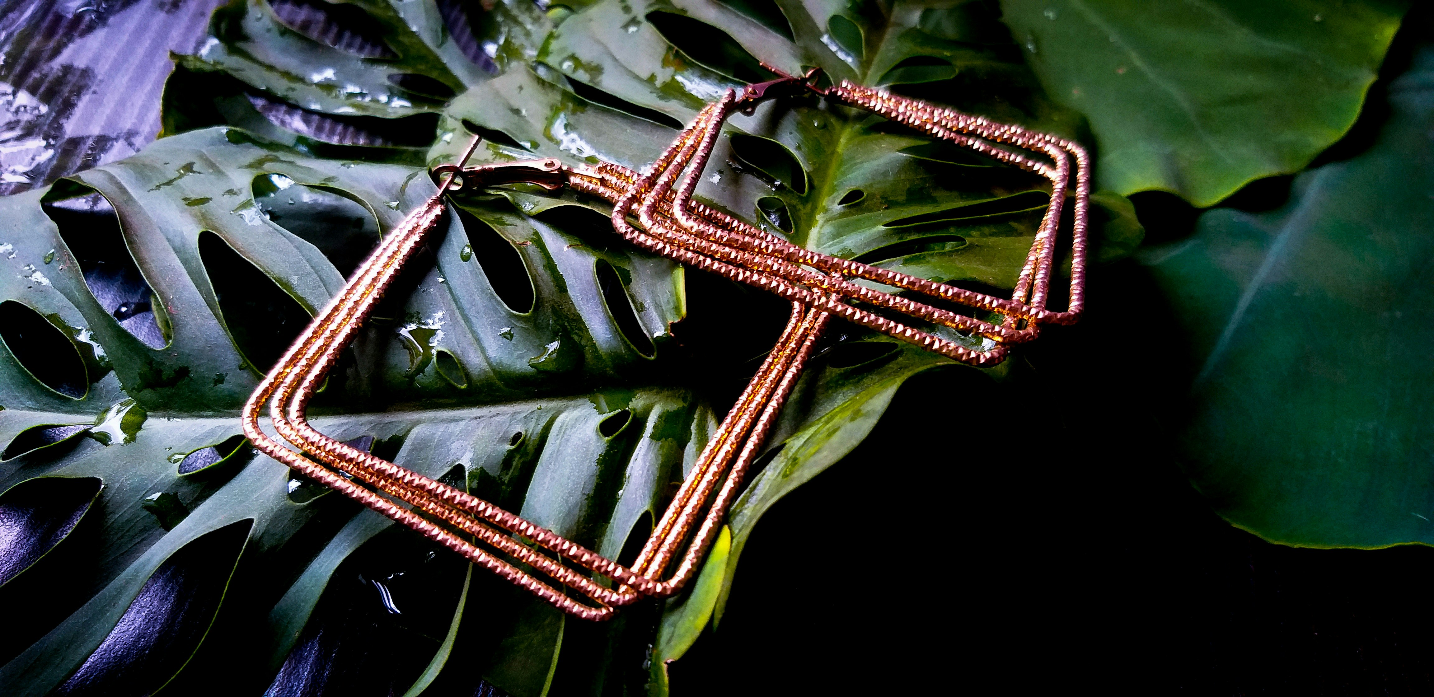 Close-up of geometric copper beaded frames laid across glossy monstera leaves, highlighting texture and metallic detail in natural light.