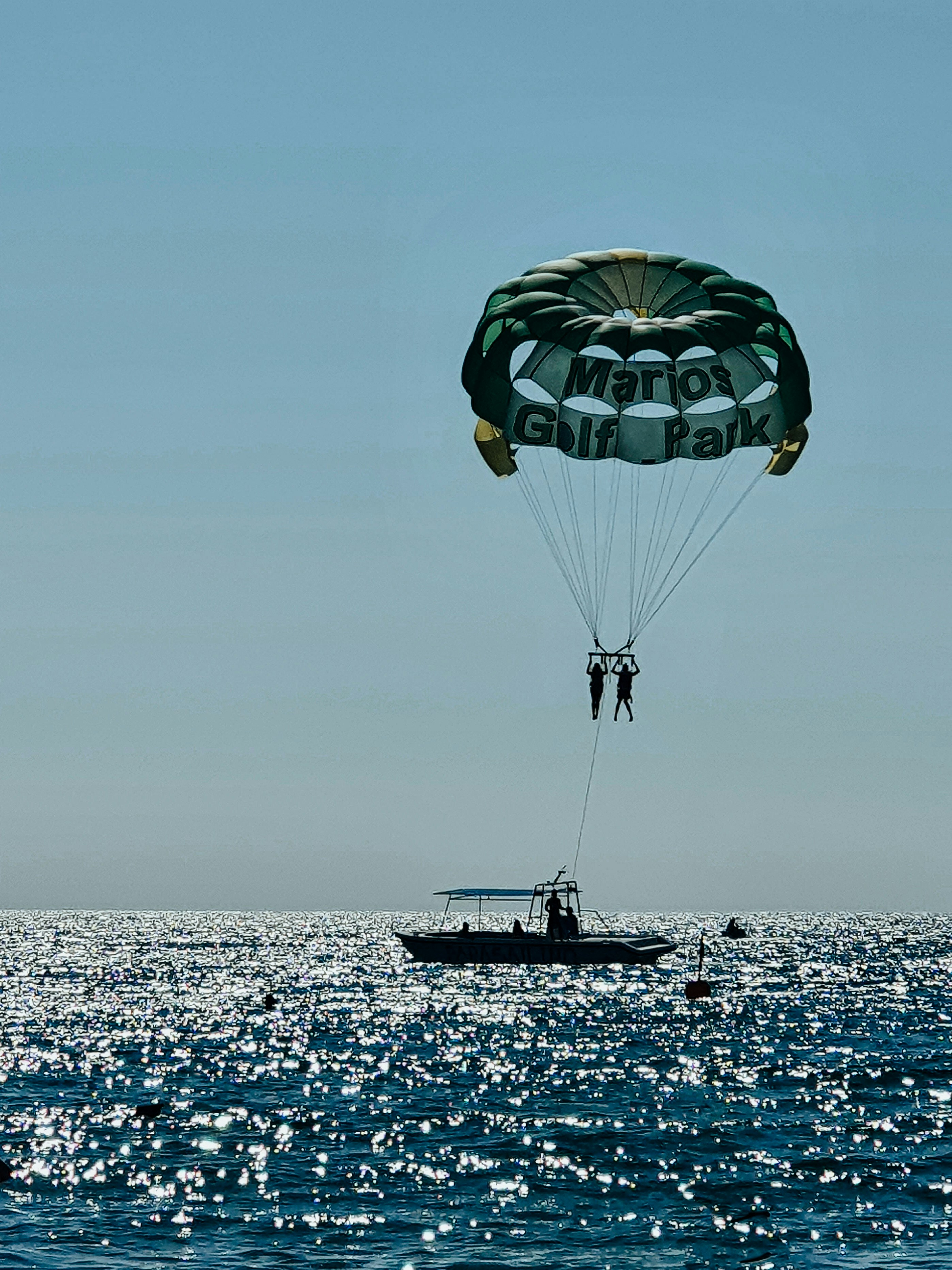Parasailing adventure with two people gliding above shimmering ocean waters, showcasing the vibrant colors of the parachute and the boat below.