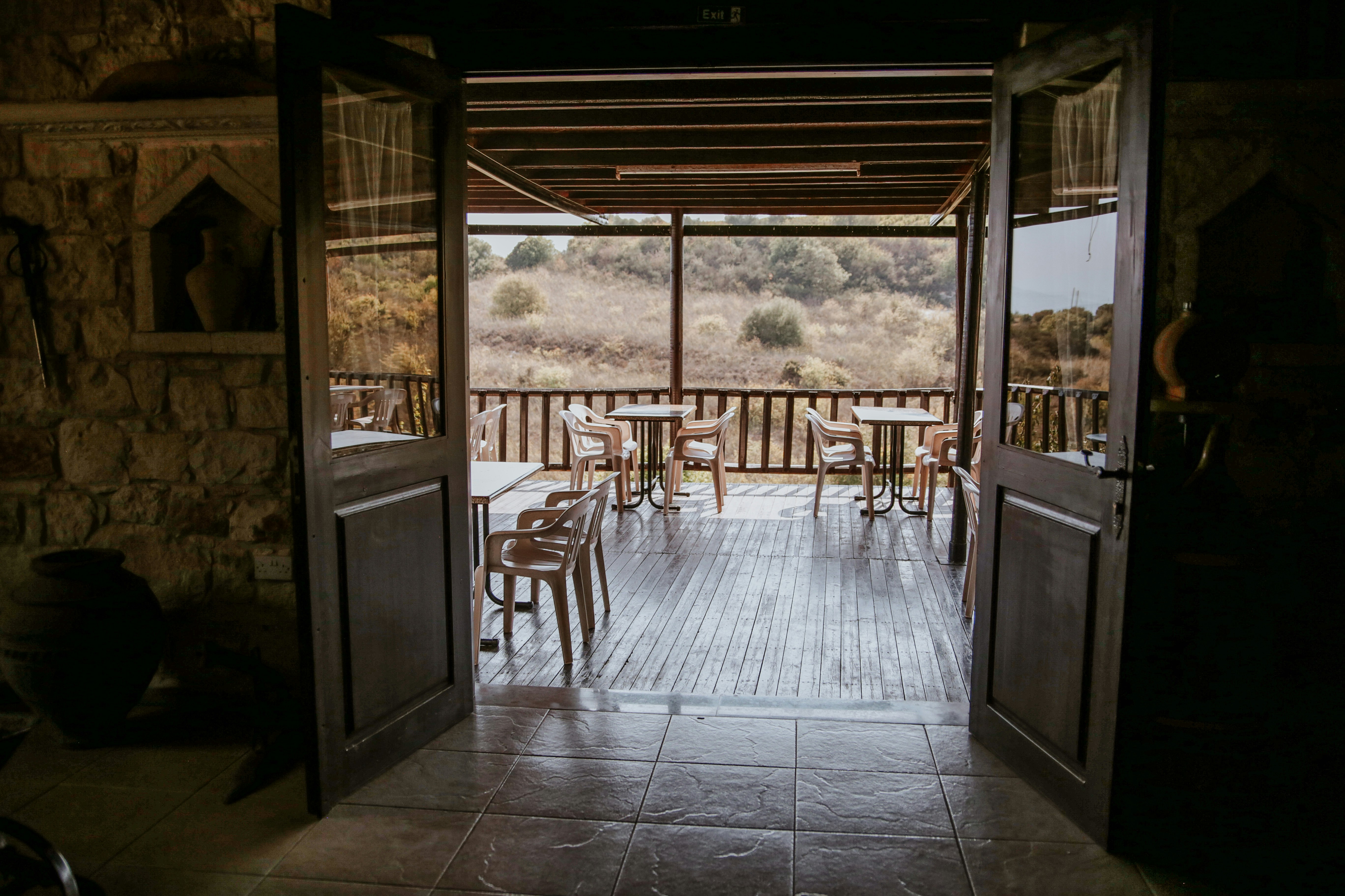 Open doors leading to a serene outdoor dining area with wooden tables and chairs overlooking distant hills.