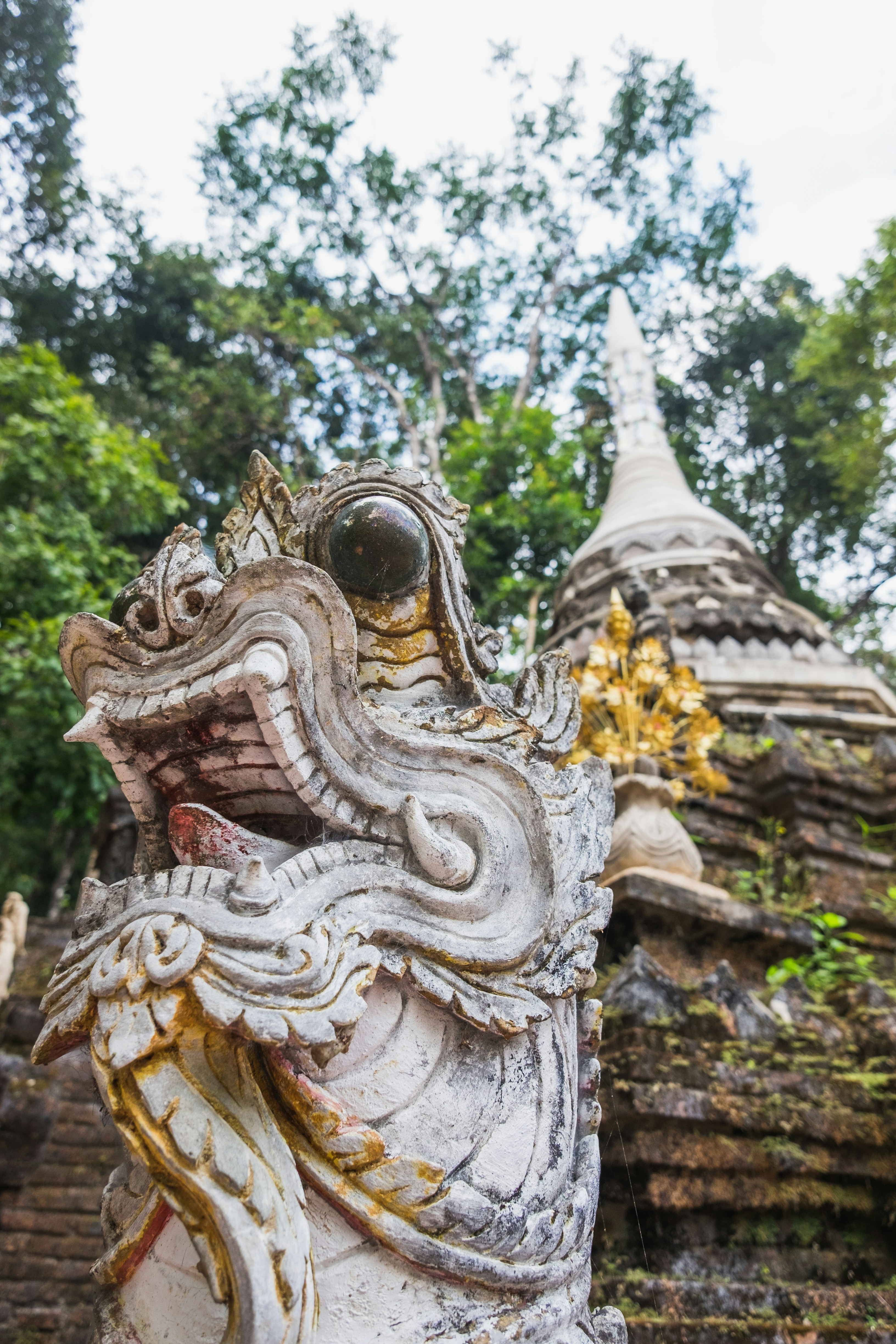 Intricate stone sculpture of a mythical creature stands at the entrance of a temple, surrounded by lush greenery and ancient architecture.