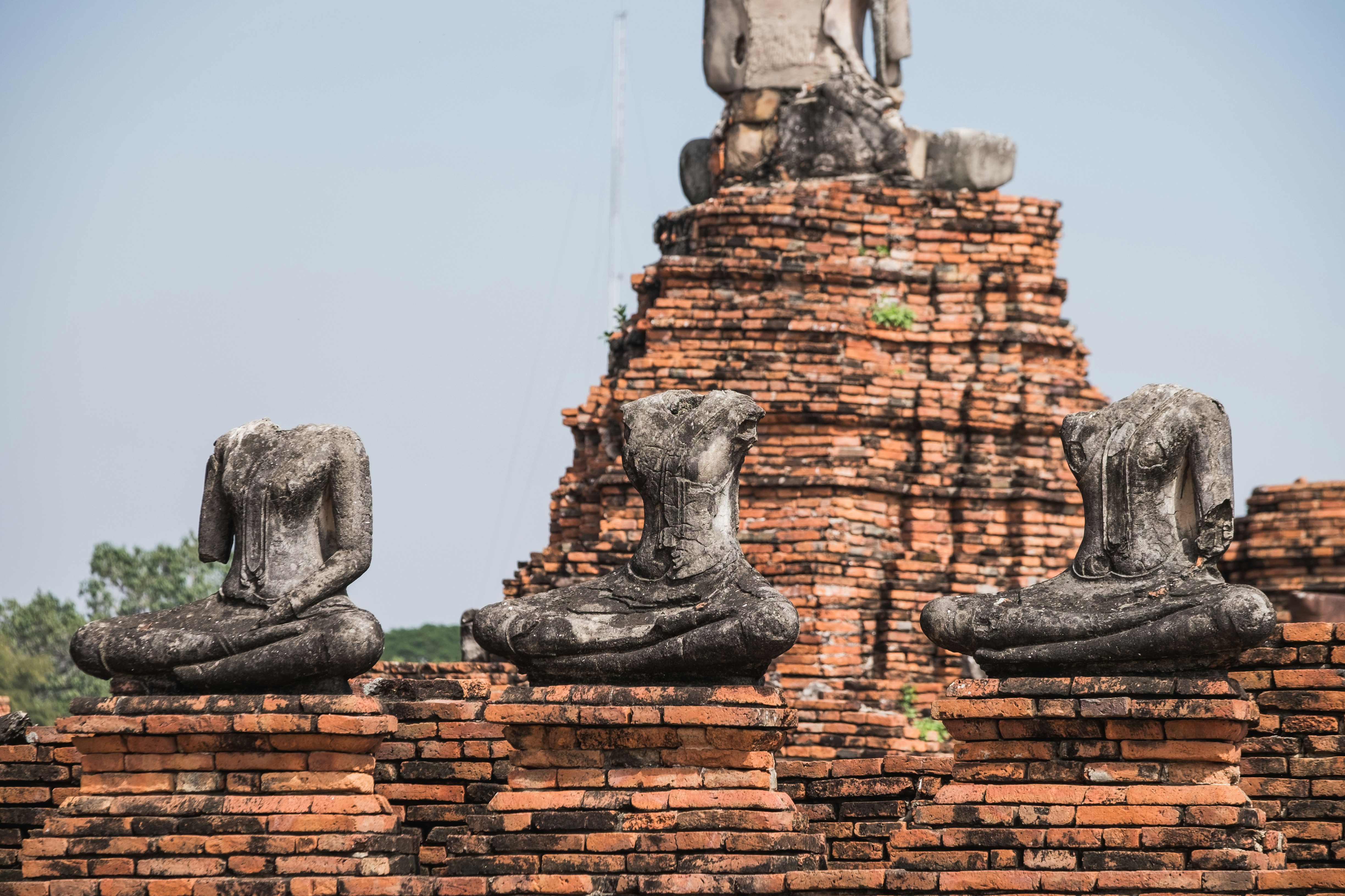 Decapitated stone Buddha statues sit atop a weathered brick structure under a clear sky.