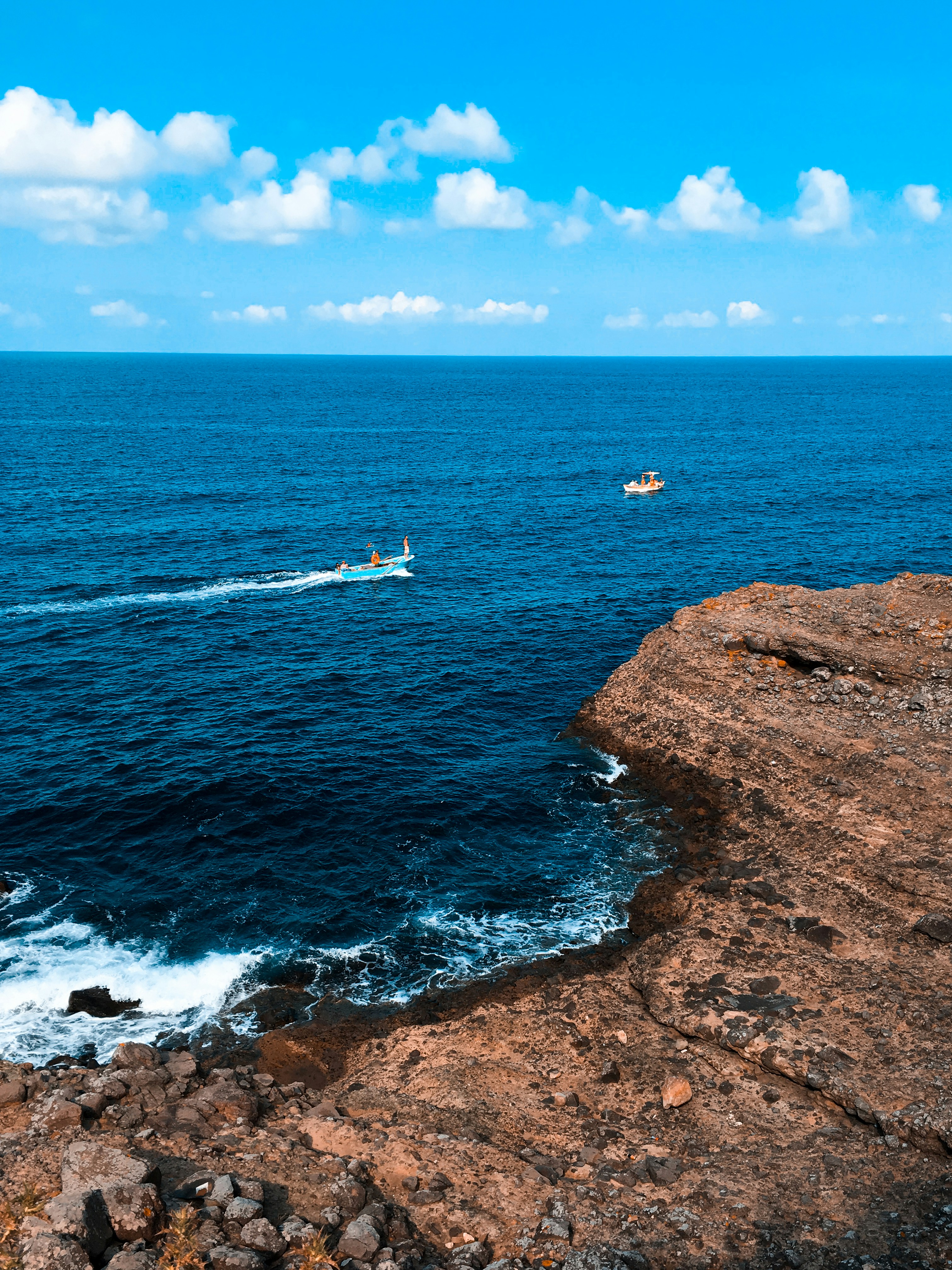 Twin Boats, Quiet Wake: A Cliffside Seascape Under Cerulean Sky