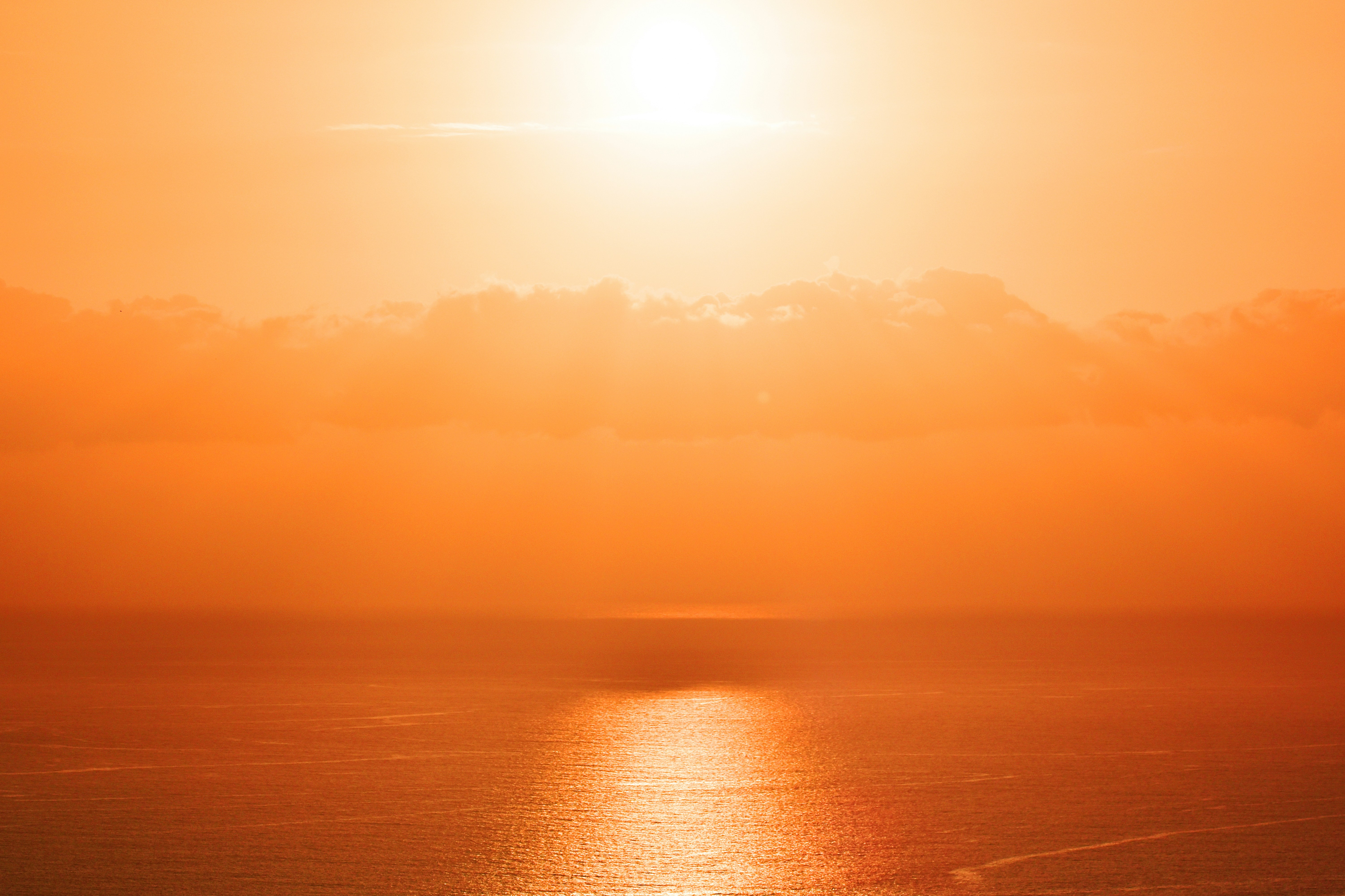 Vibrant sunset casting warm orange hues over calm ocean waters, with soft clouds reflecting the light. The serene scene invites tranquility.