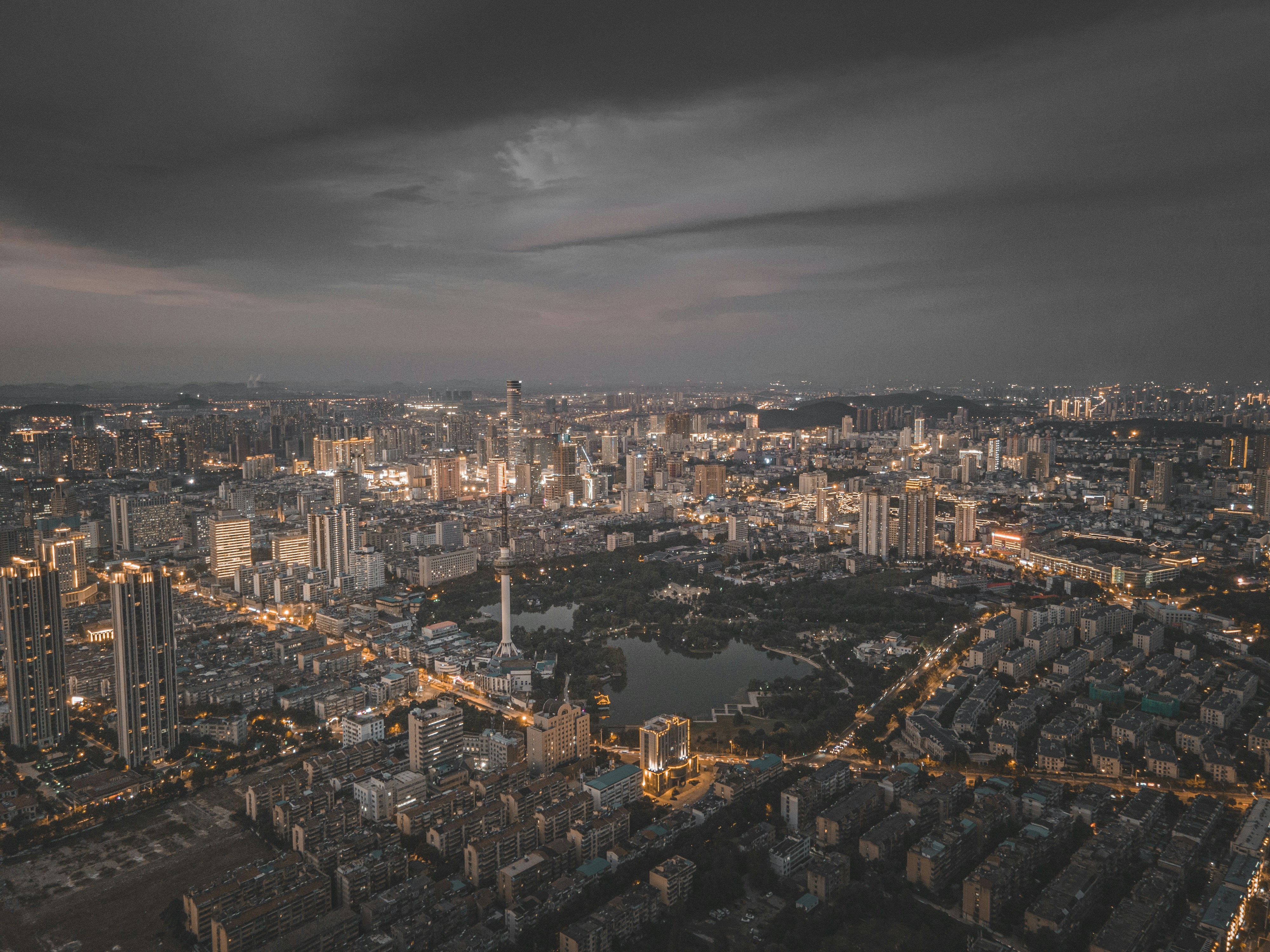 Expansive cityscape with illuminated buildings and roads under a dramatic cloudy sky at dusk.