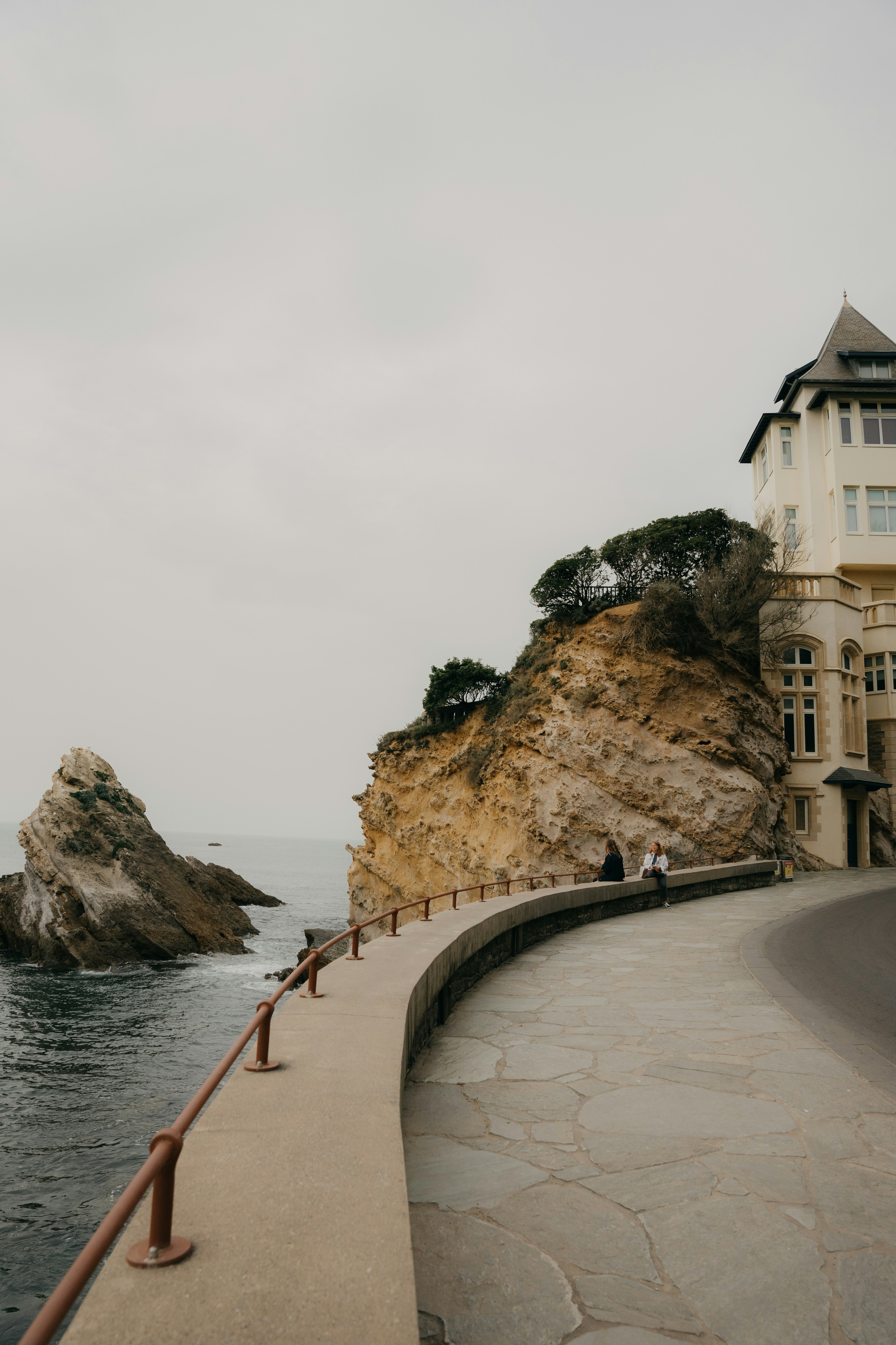 A stone walkway with buildings and a cliff with a body of water photo ...