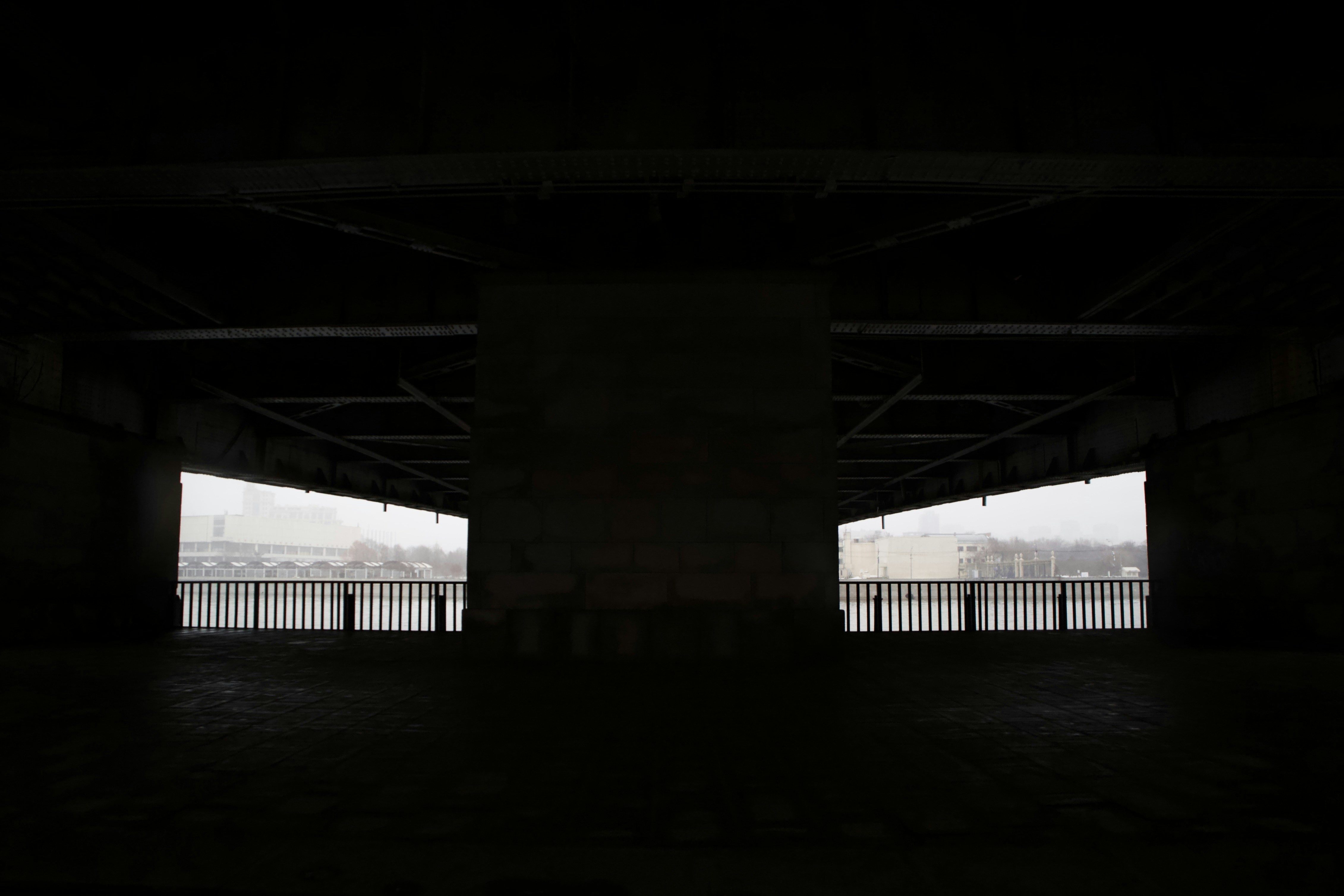 Silhouette of a bridge's understructure with misty river view in the background. The scene conveys a sense of mystery and isolation.